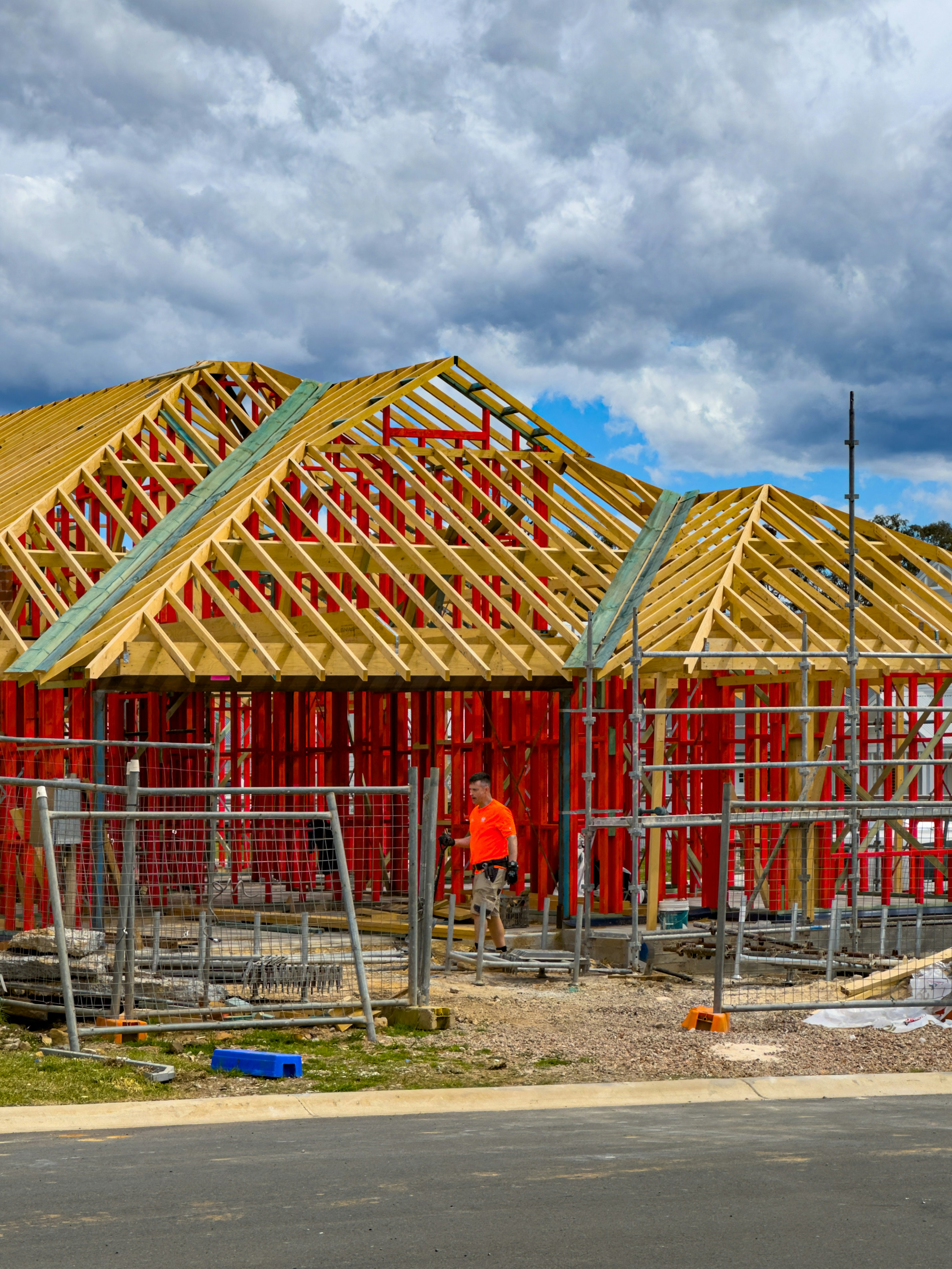 Under Construction: Yellow Timber Roof Frames Rise Over Fenced Site