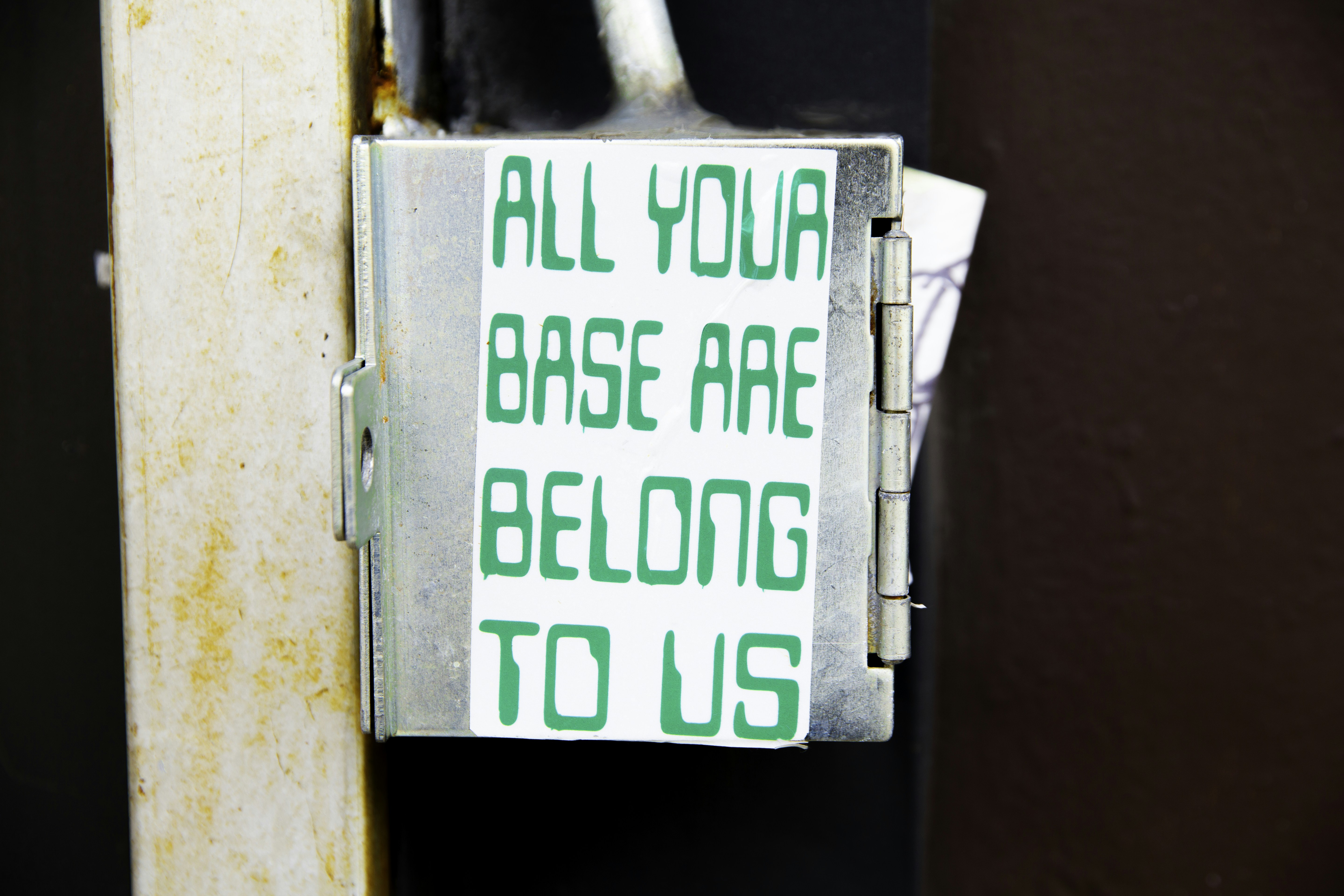 Green-lettered sign: All Your Base Are Belong To Us on an old metal box