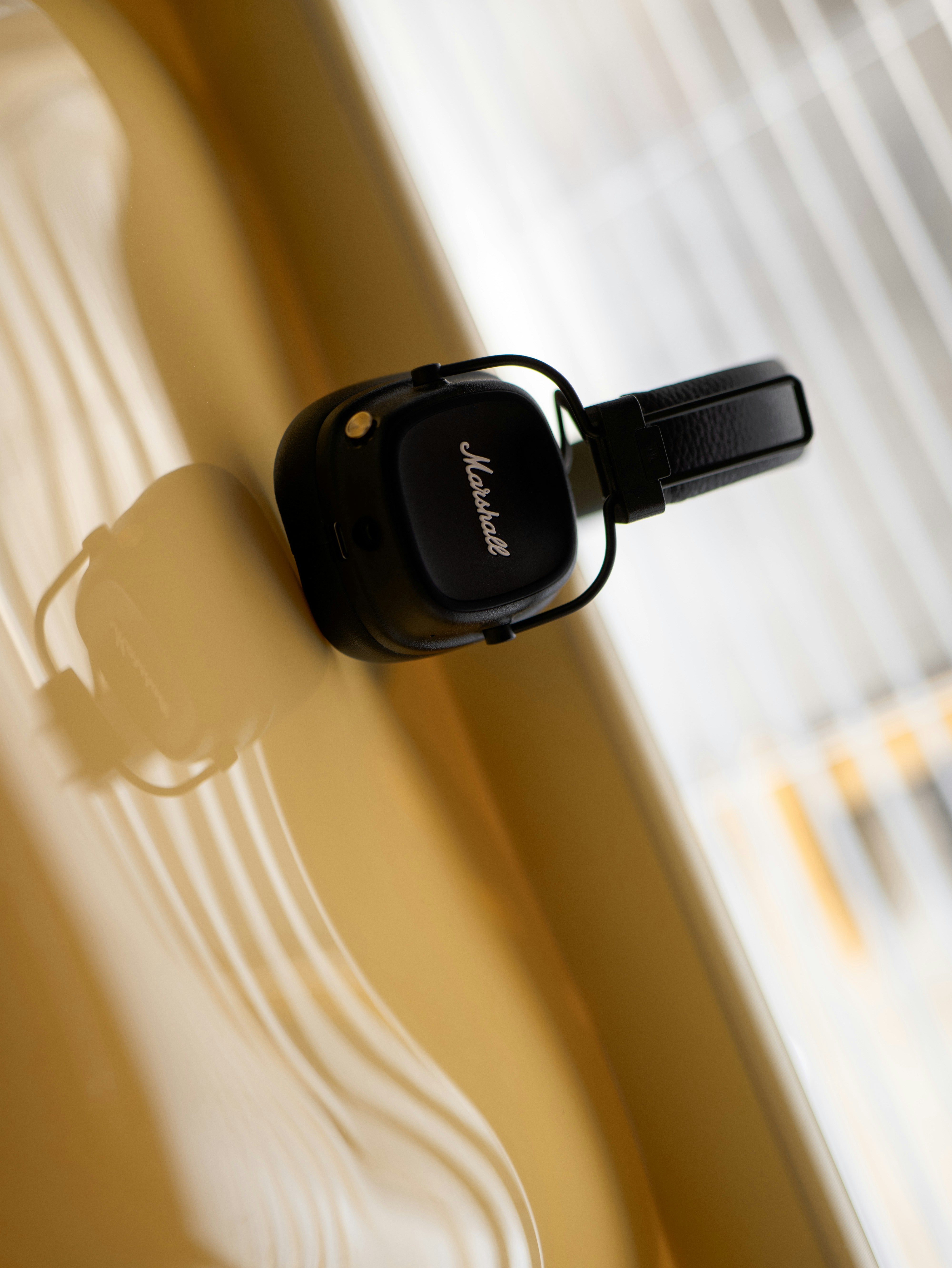 Black Jackson headphones rest on a glossy, wavy surface with soft warm light