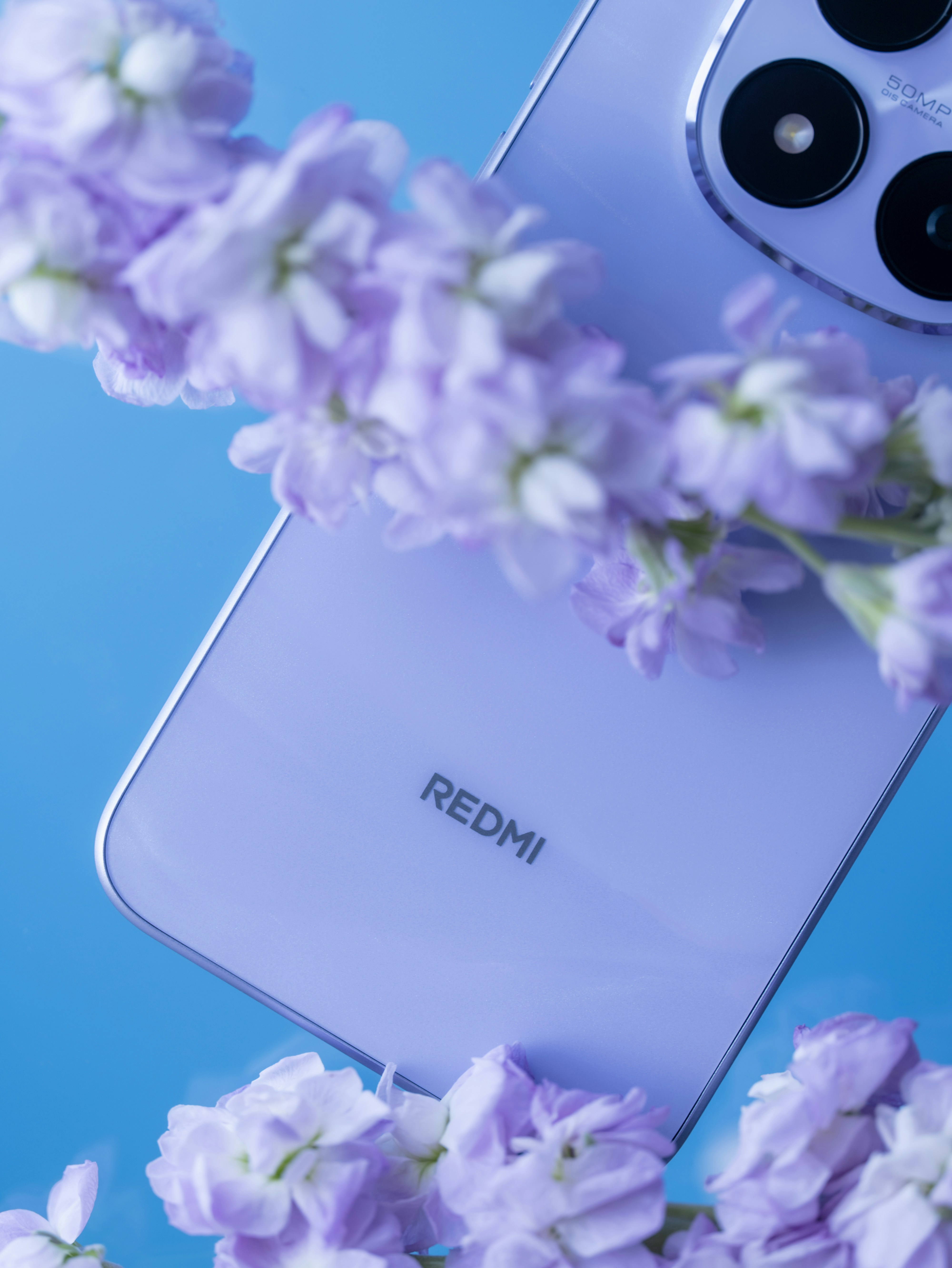 Purple-flowered frame: a Redmi phone resting among blossoms on a blue backdrop
