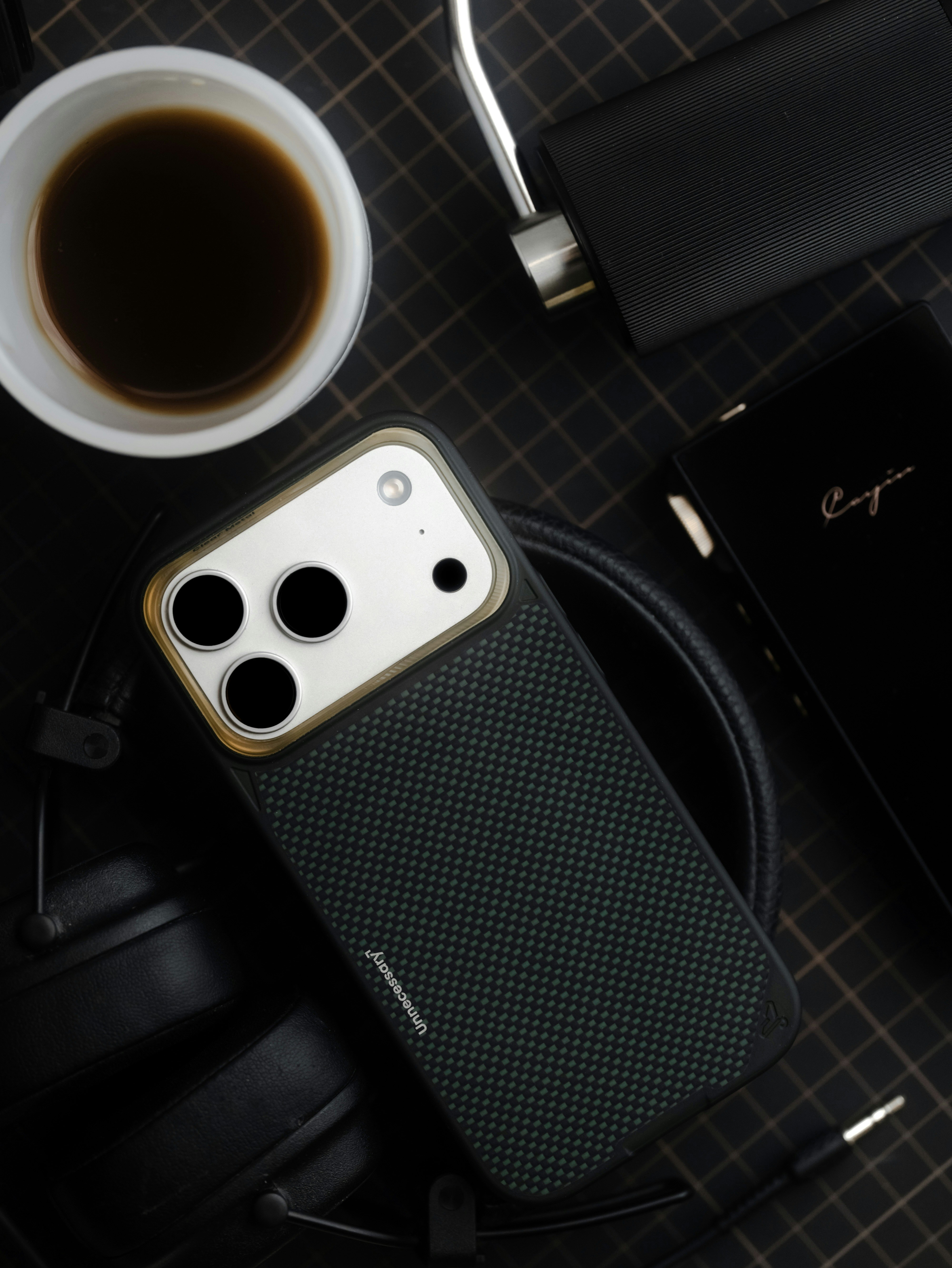 Triple-lens iPhone resting beside a coffee cup and headphones