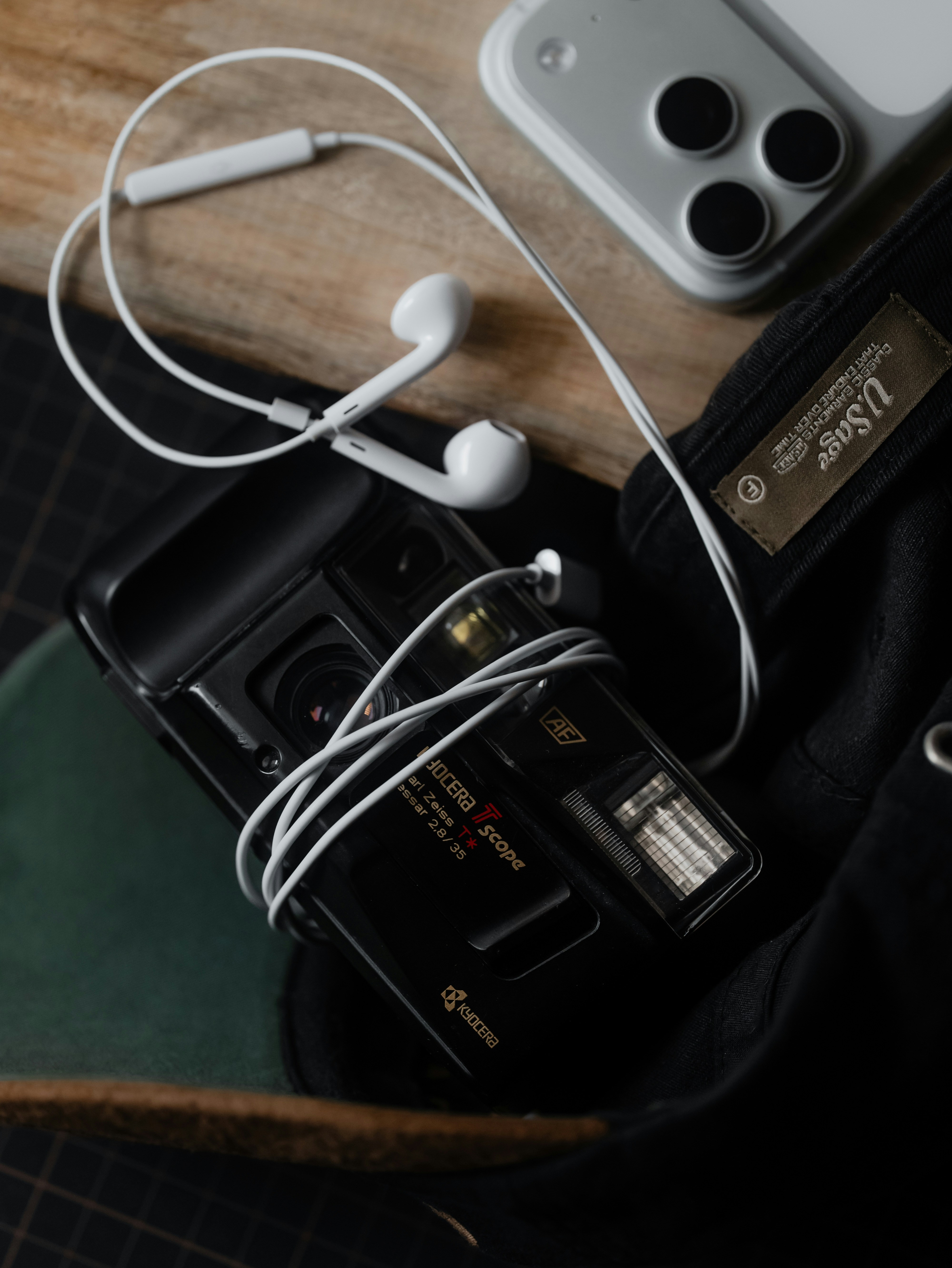 Close-Up of a Vintage Film Camera Nestled with Modern Earbuds and an iPhone Case