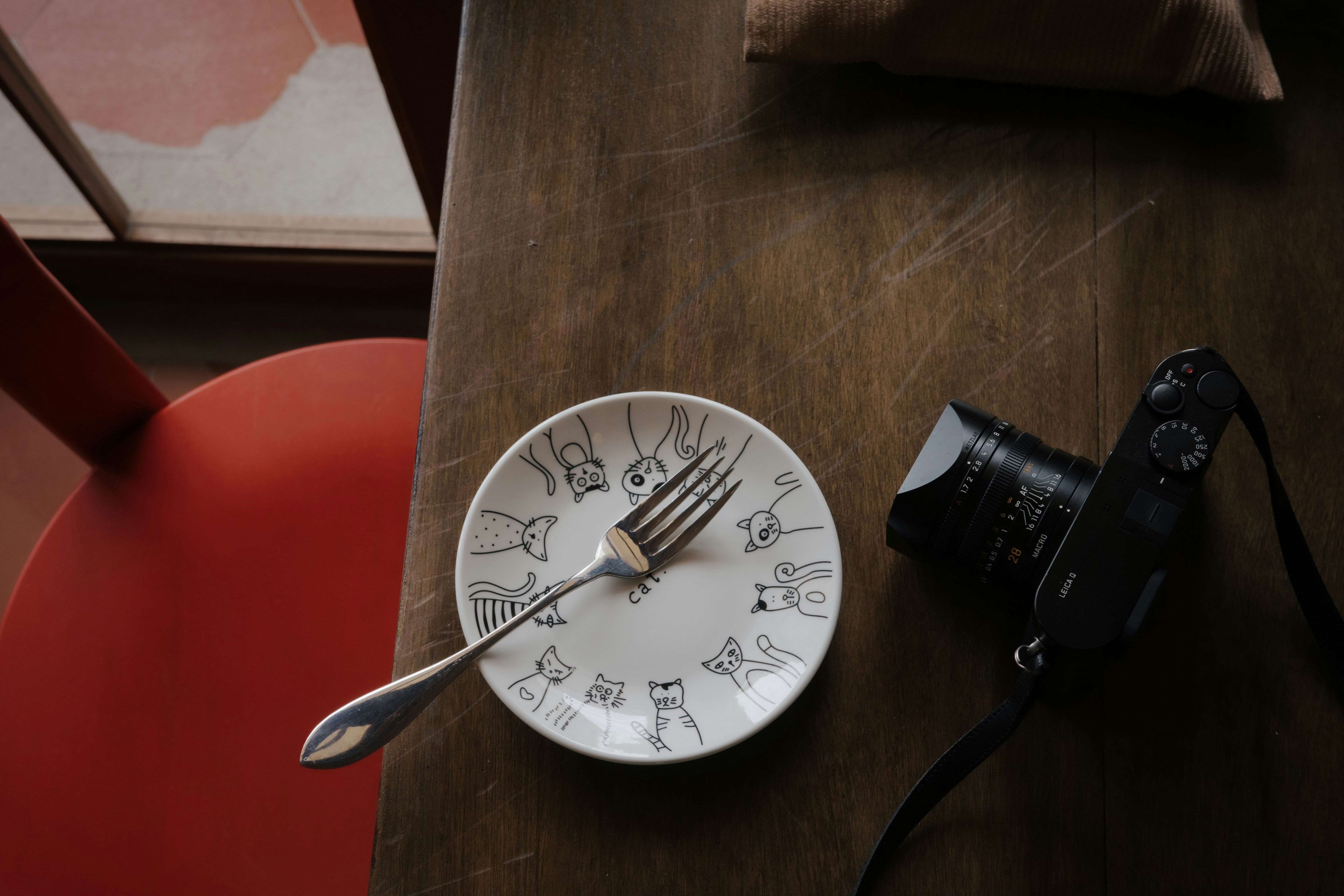 Midday still life: plate, fork, and a compact camera on a wooden table