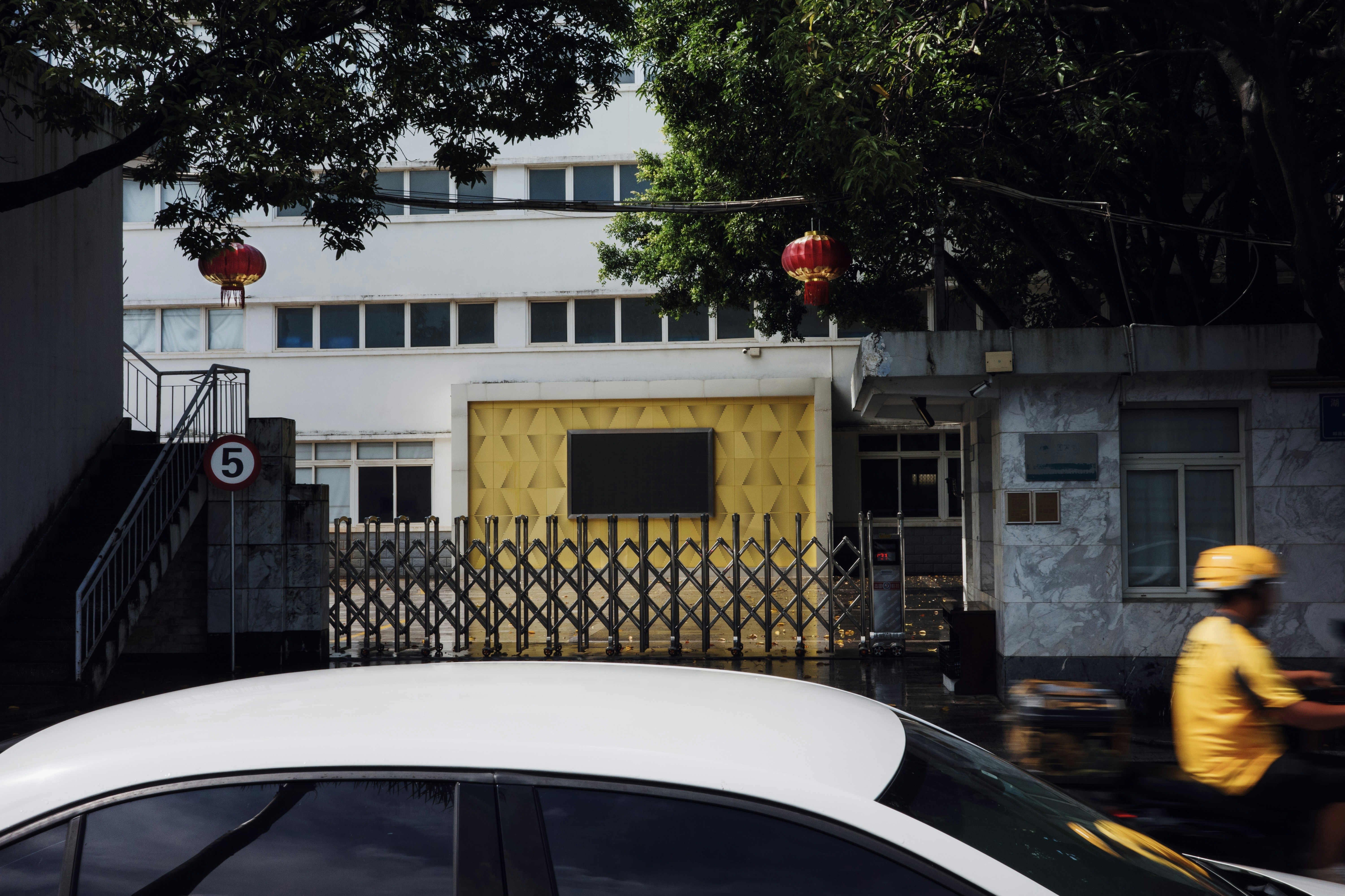 A white car passes a building with red lanterns.