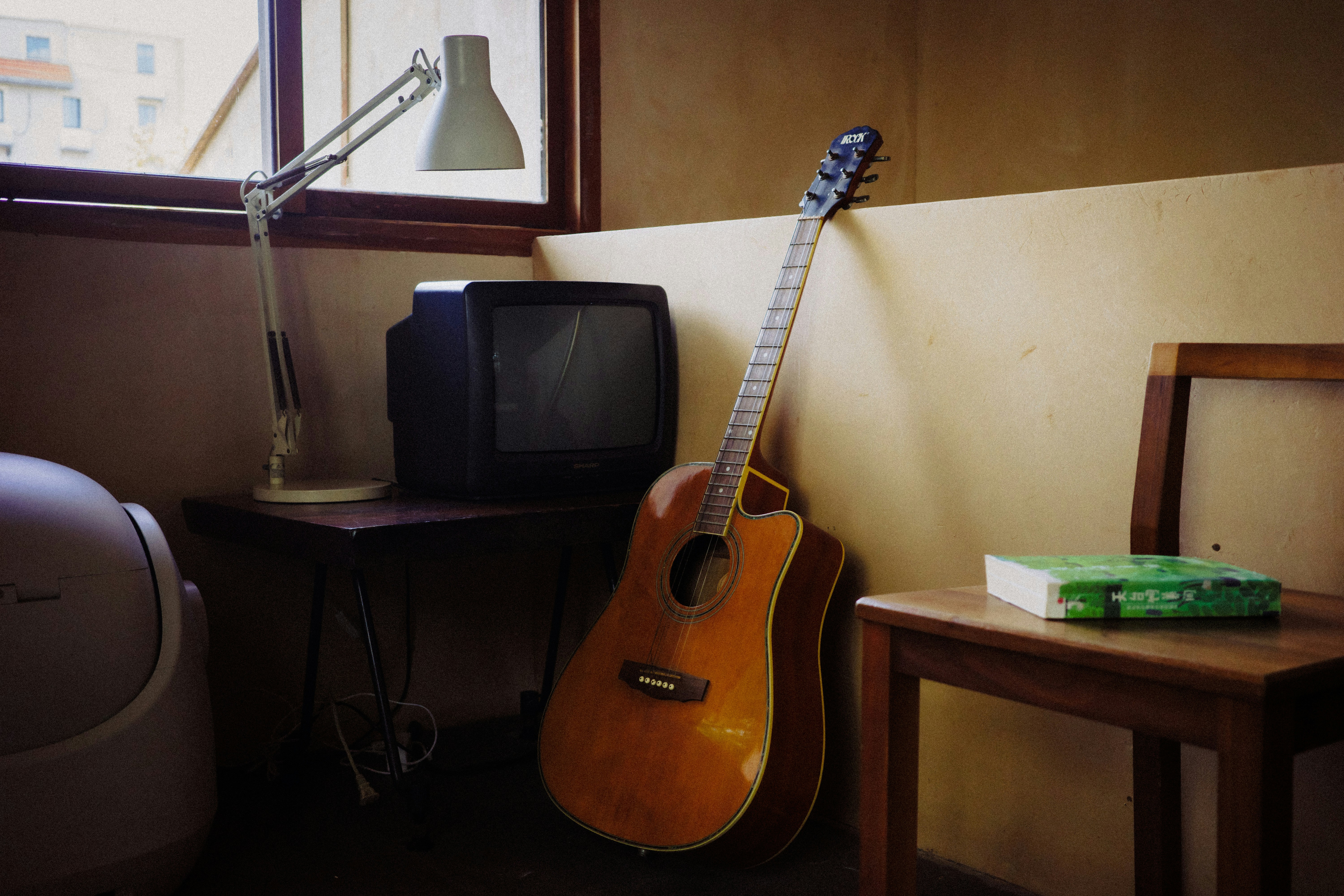 Warm-room Serenade: An Acoustic Guitar Stands Vigil beside Retro Screen