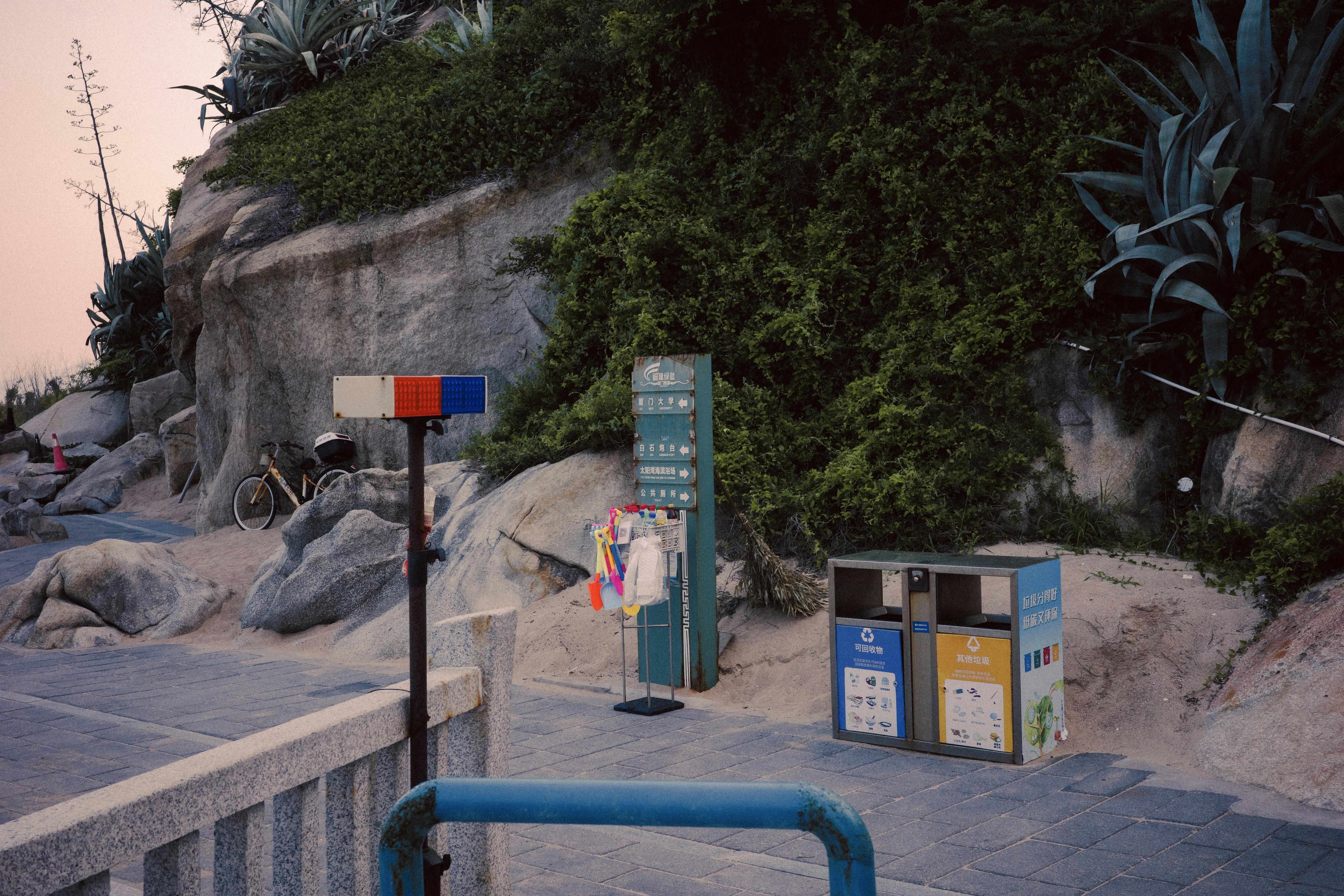 Blue railing leading to a sunlit coastal stair with a distant cyclist and signposts