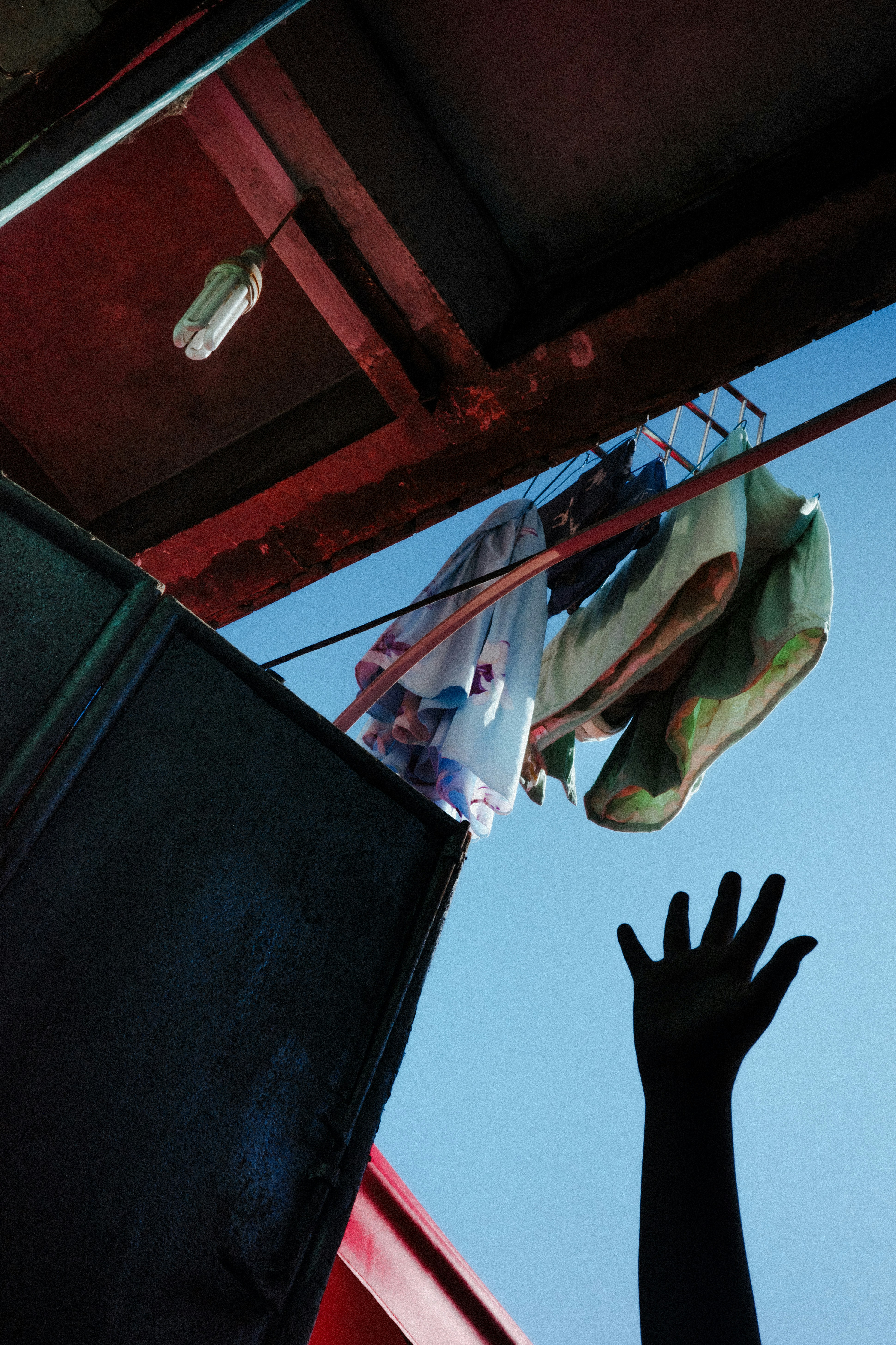 Outstretched Shadow: Hand Reaching Toward Sunlit Laundry under a Rusted Overhang