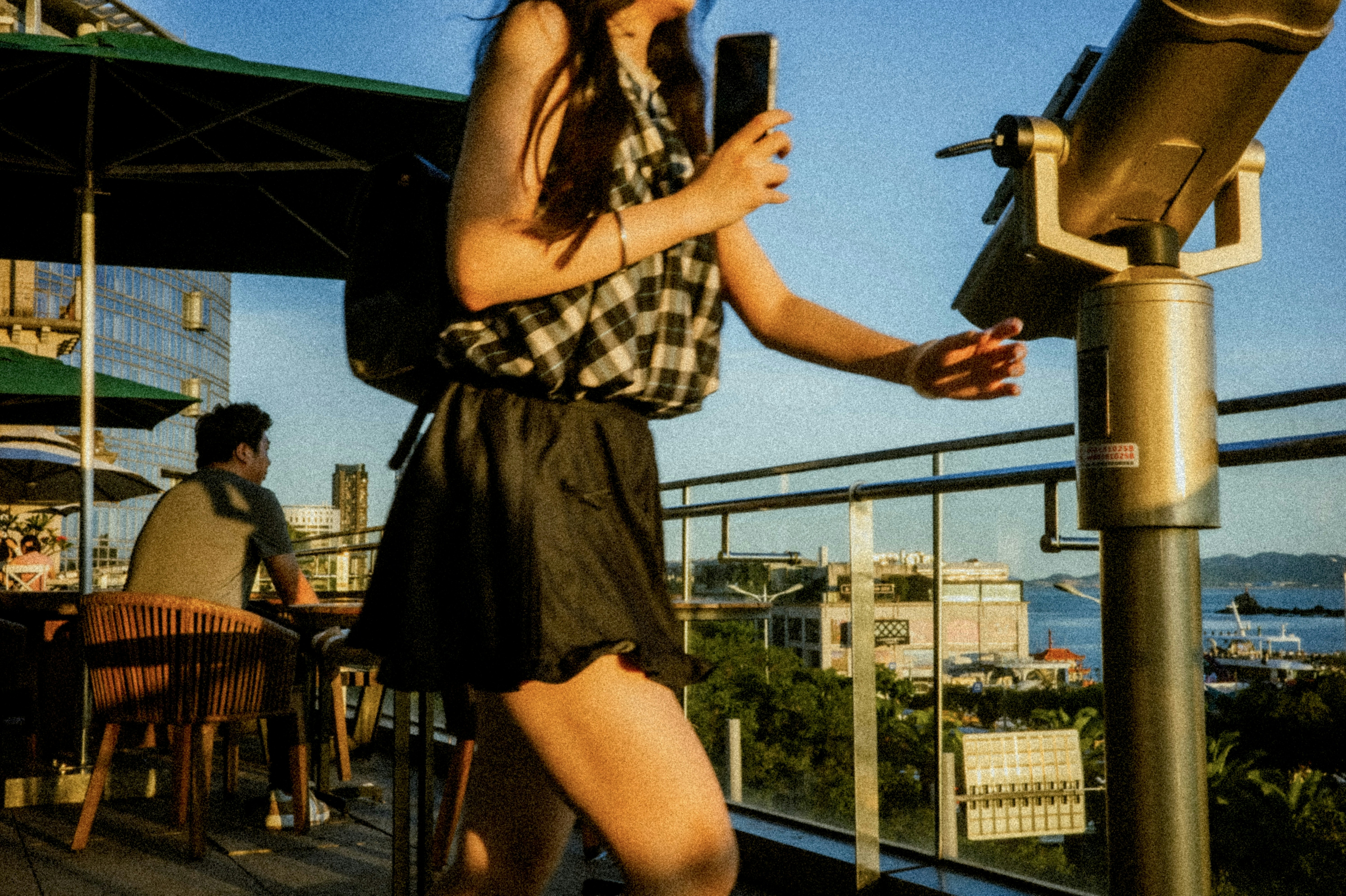 Woman taking photo with smartphone on balcony near telescope.