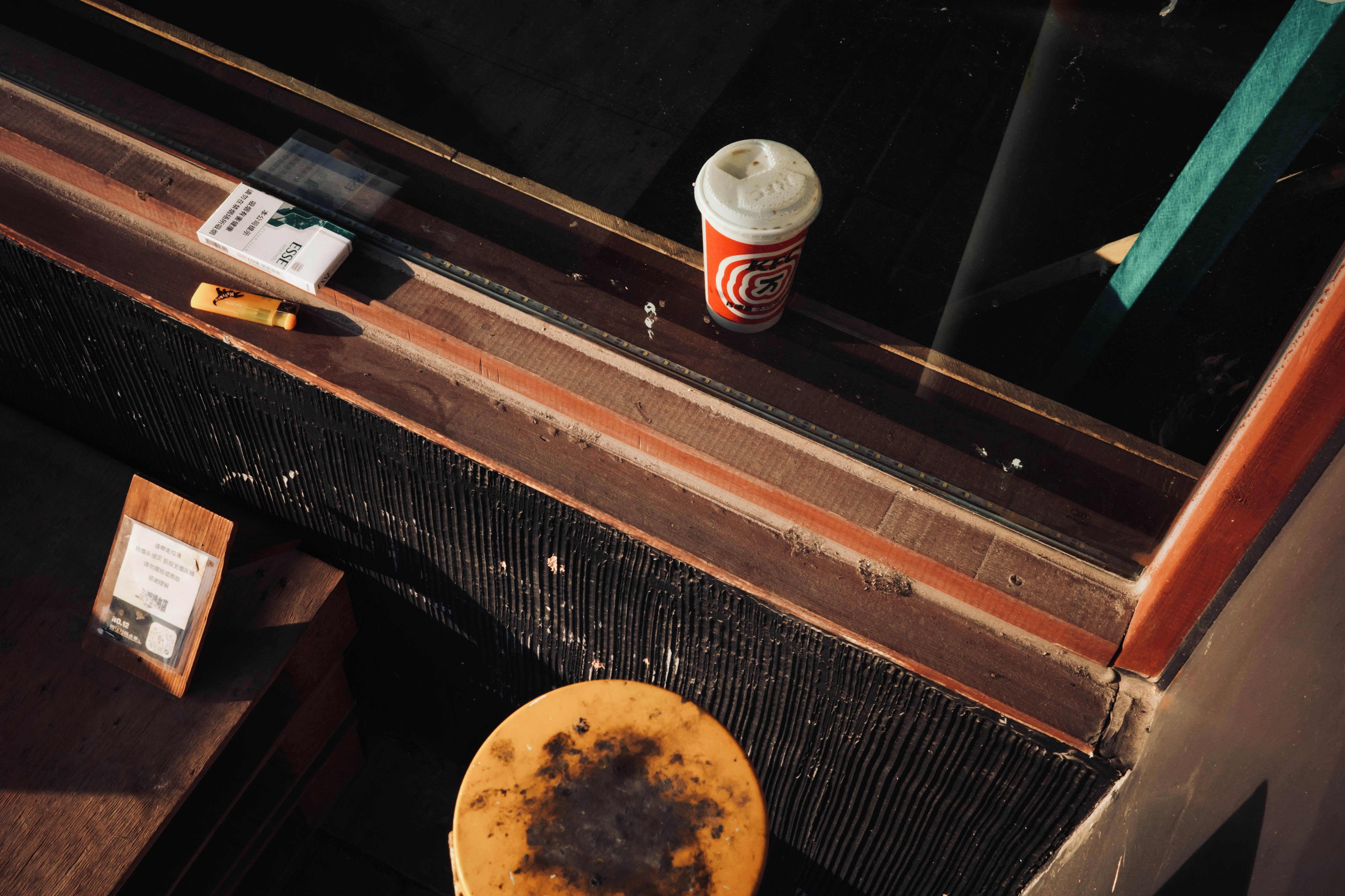 A dimly lit urban corner: cigarette pack, coffee cup, and a weathered bar edge