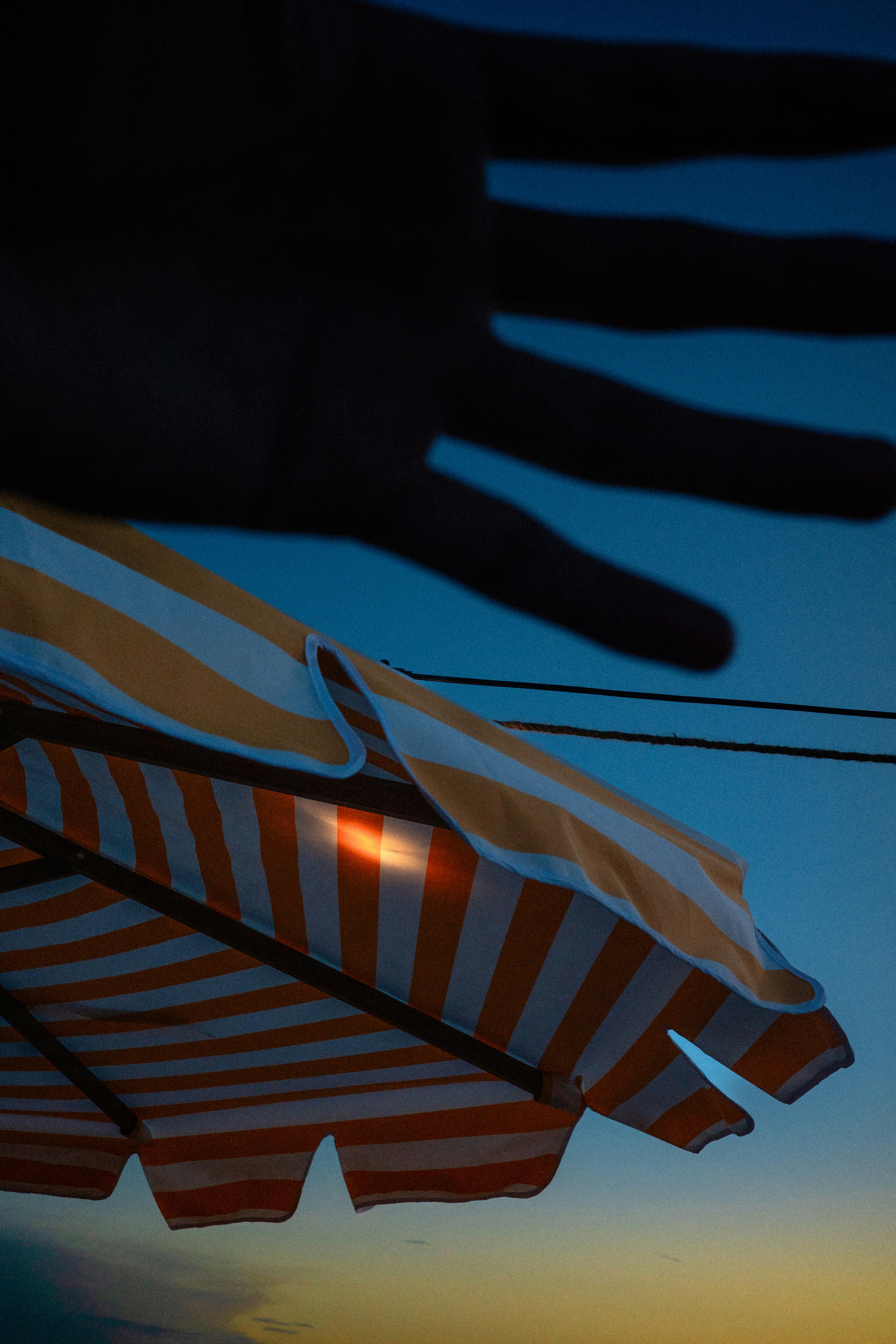 Hand shadow and striped umbrella against a twilight sky.