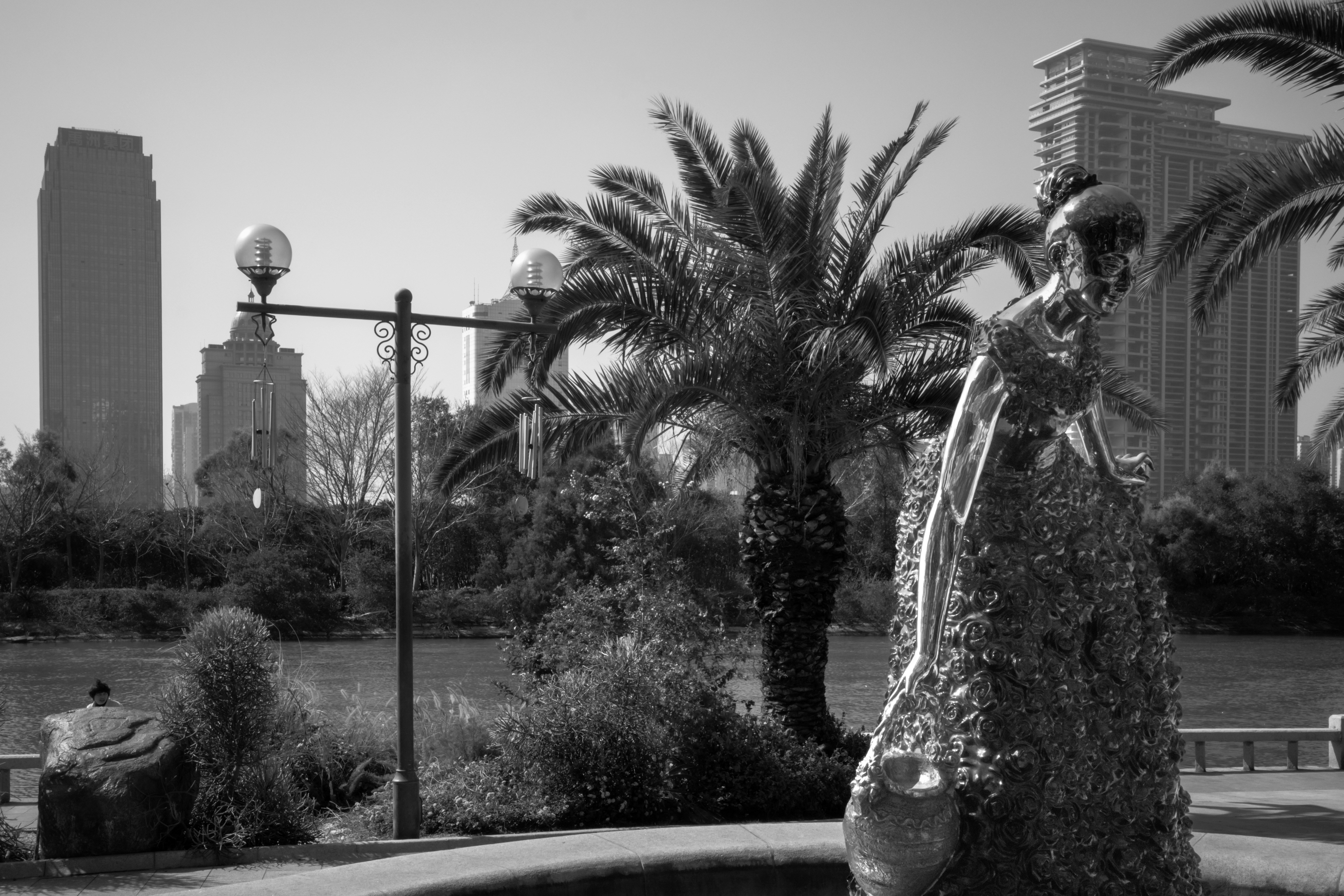 Metallic Grace by the River: A Sculpted Figure in the Urban Oasis