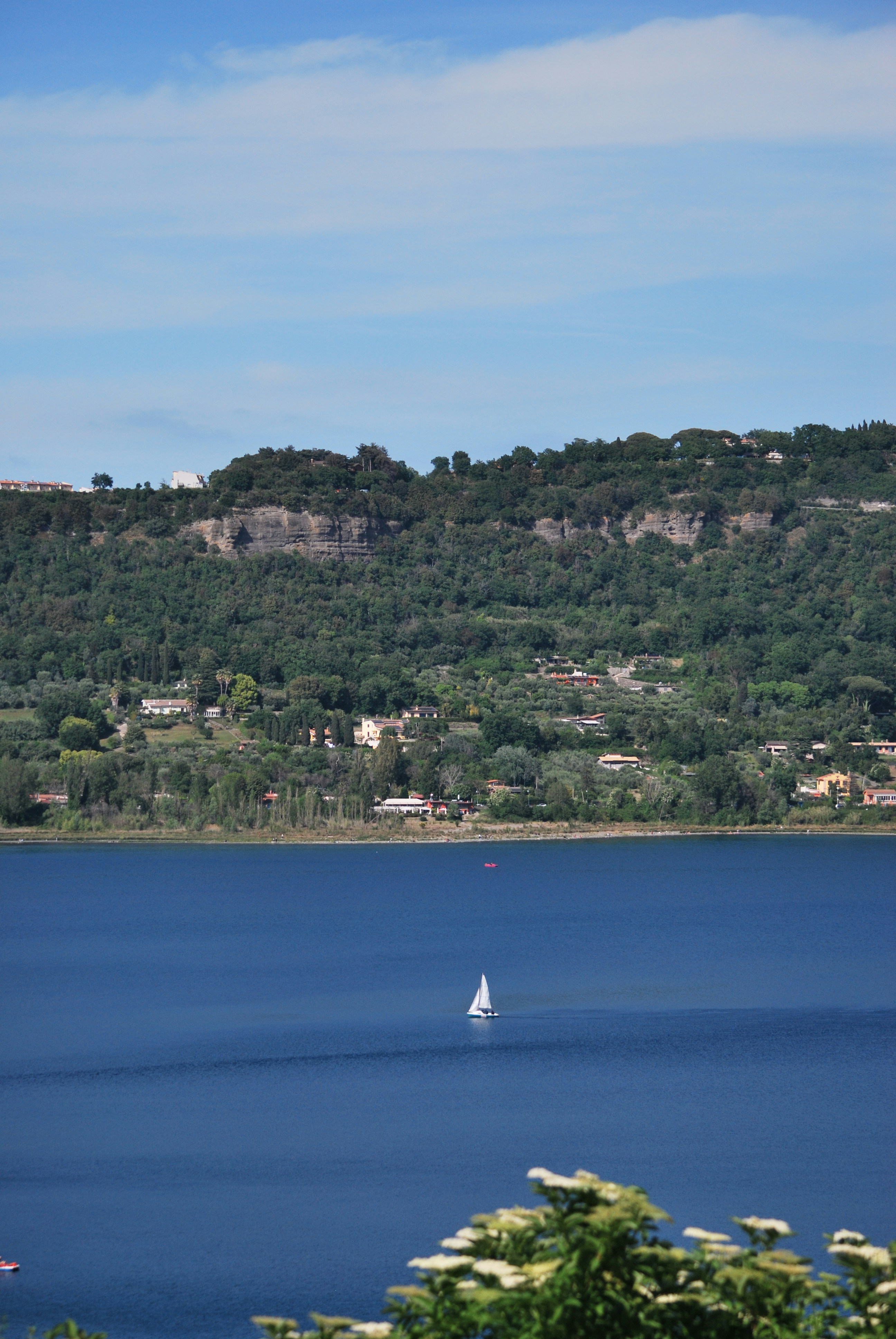 Blue Expanse and Green Cliffs: A Serene Lakeside Sail