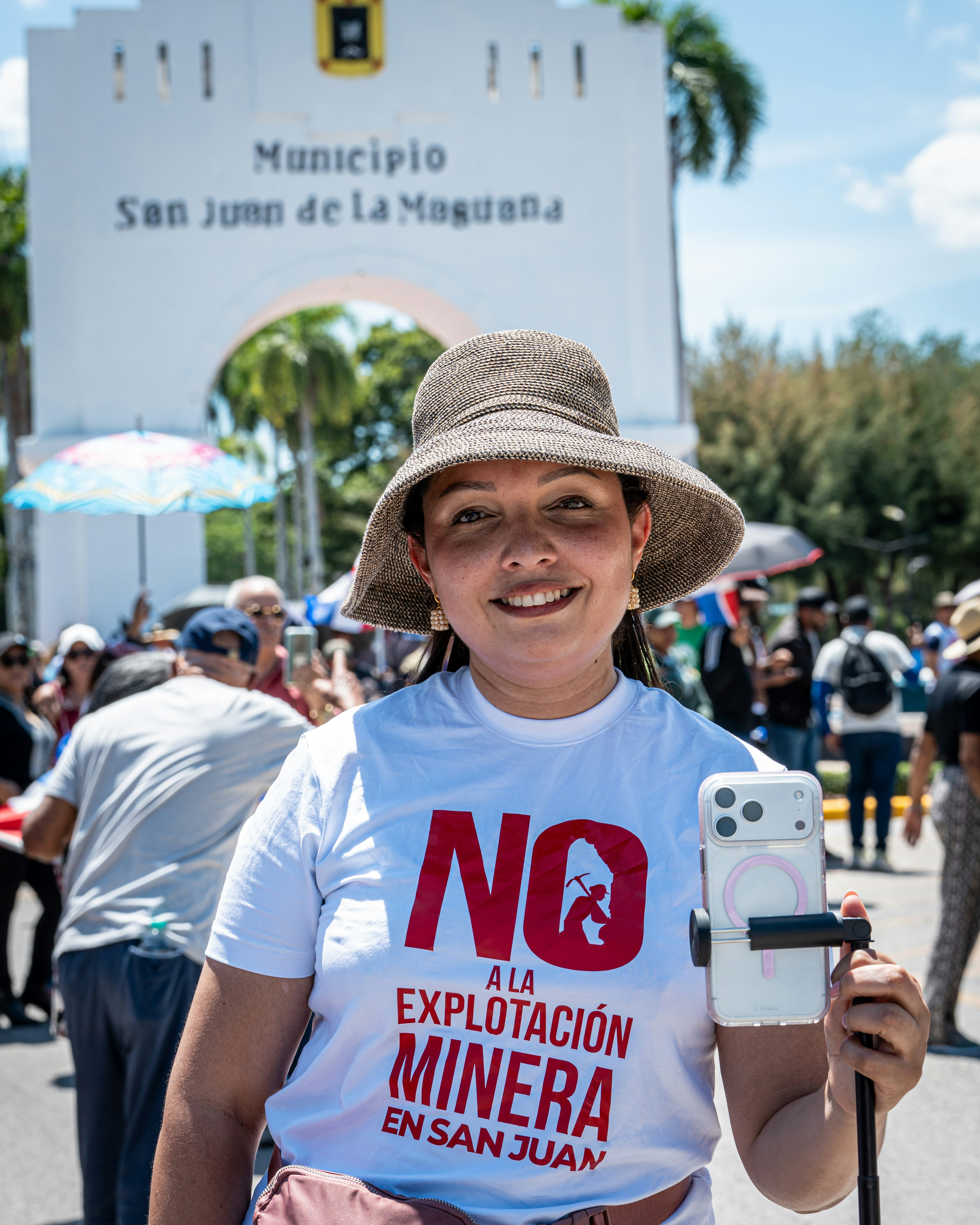 Smiling protester in sunhat at the town arch, recording the moment