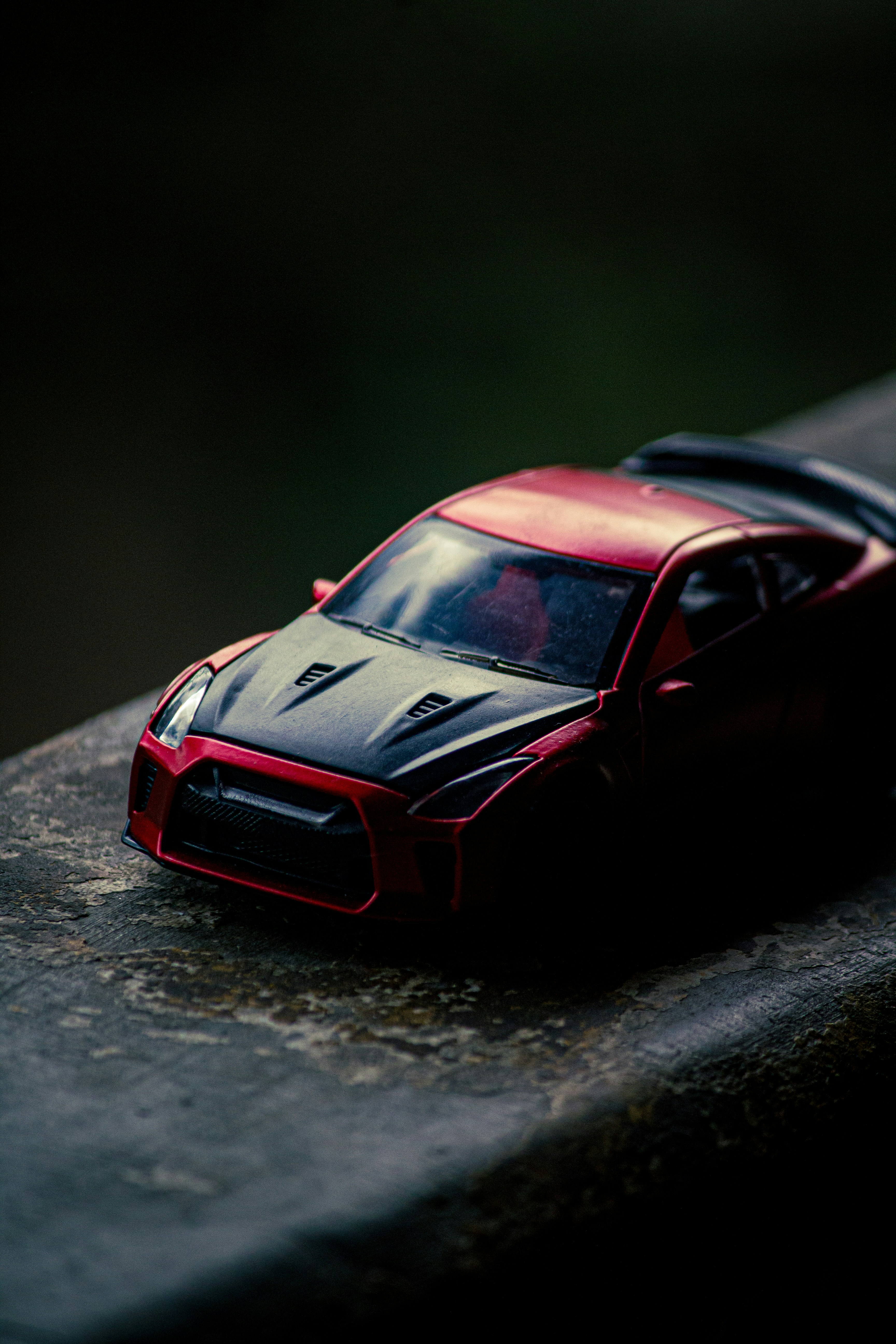 Red toy car on a weathered ledge with moody depth