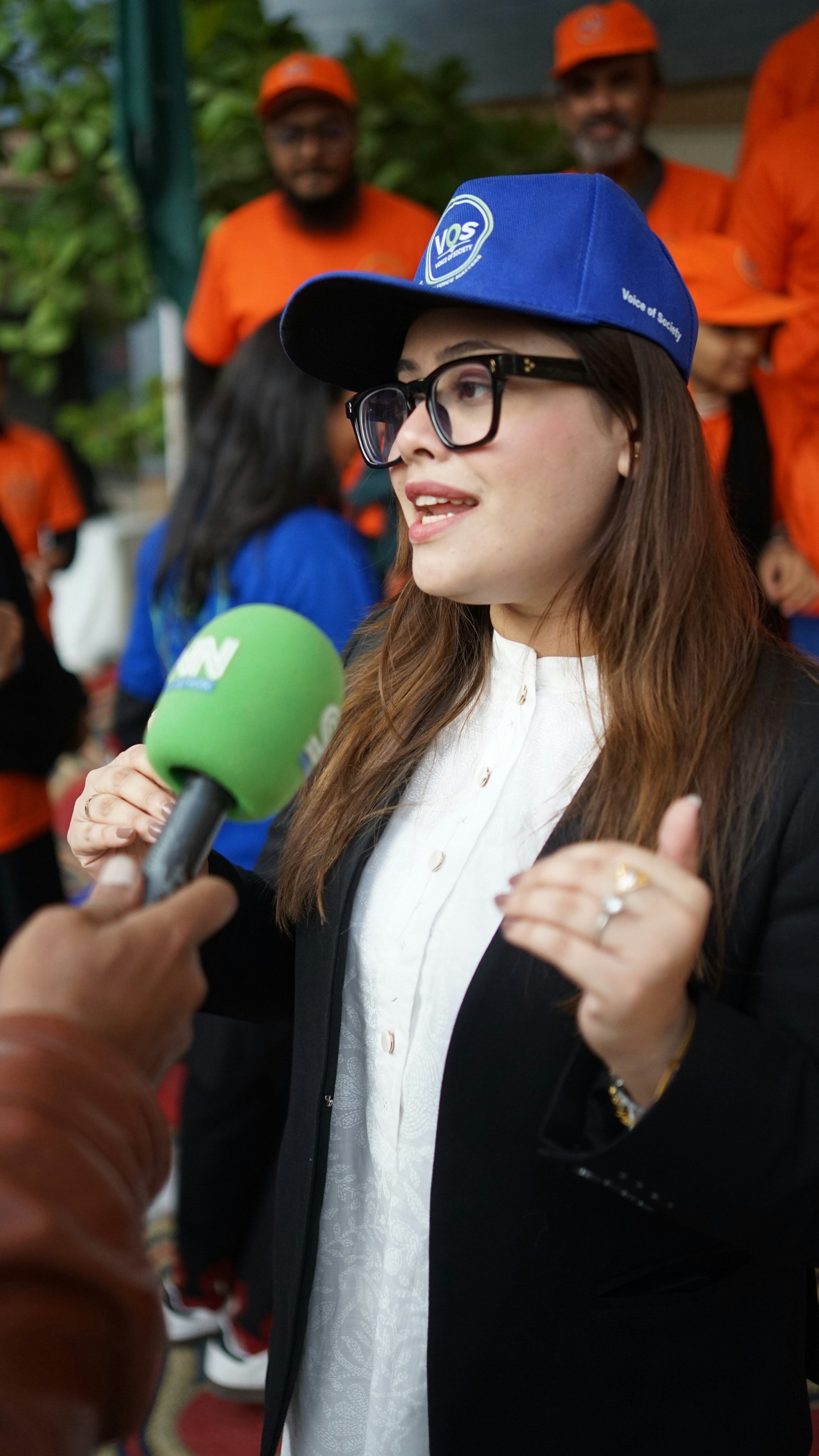 Interview in Focus: The Reporter in a Blue Cap Amid Orange-Hued Crowd