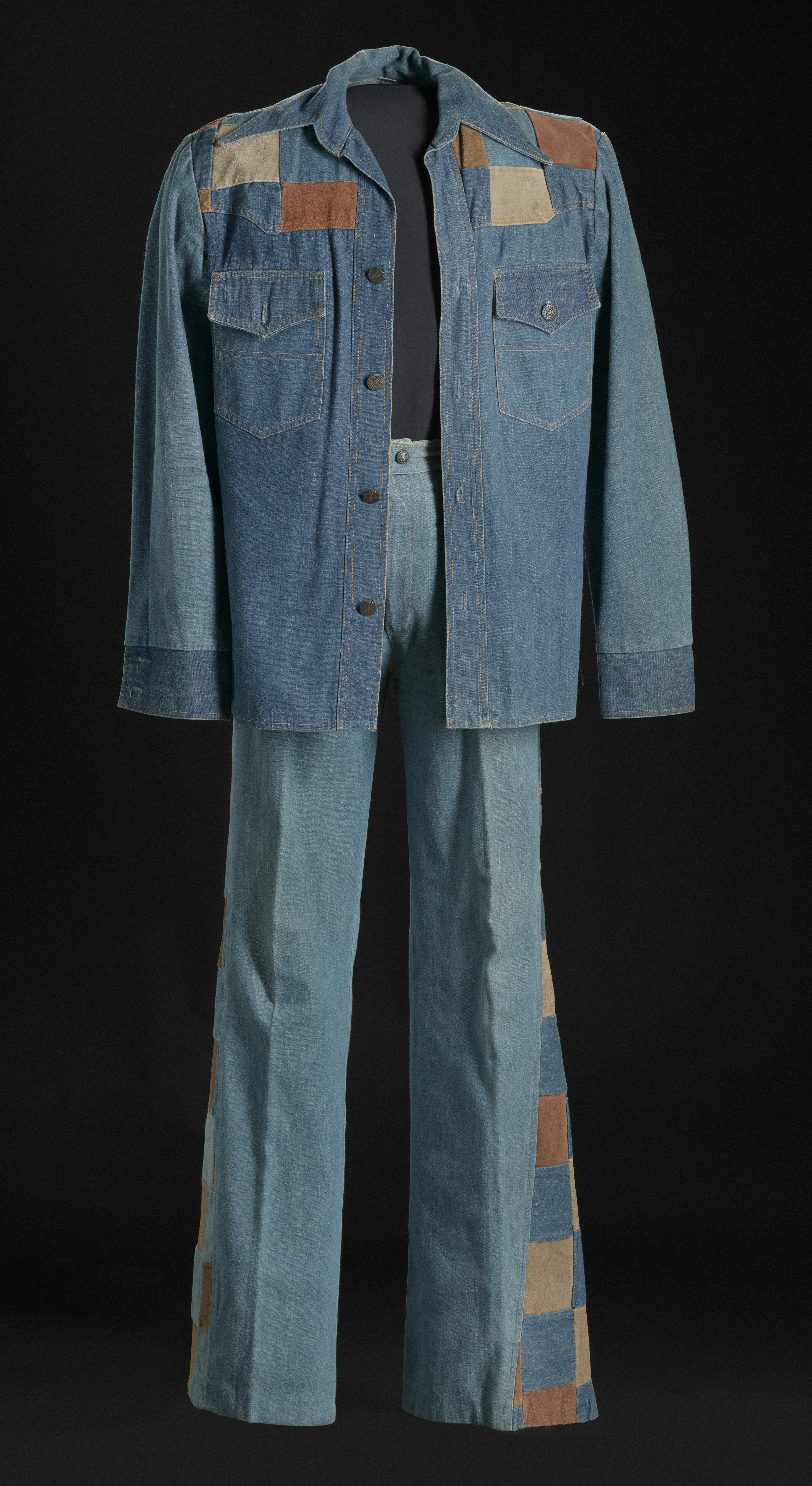 Patchwork Denim Ensemble on a Stand, Centered Against a Dark Backdrop
