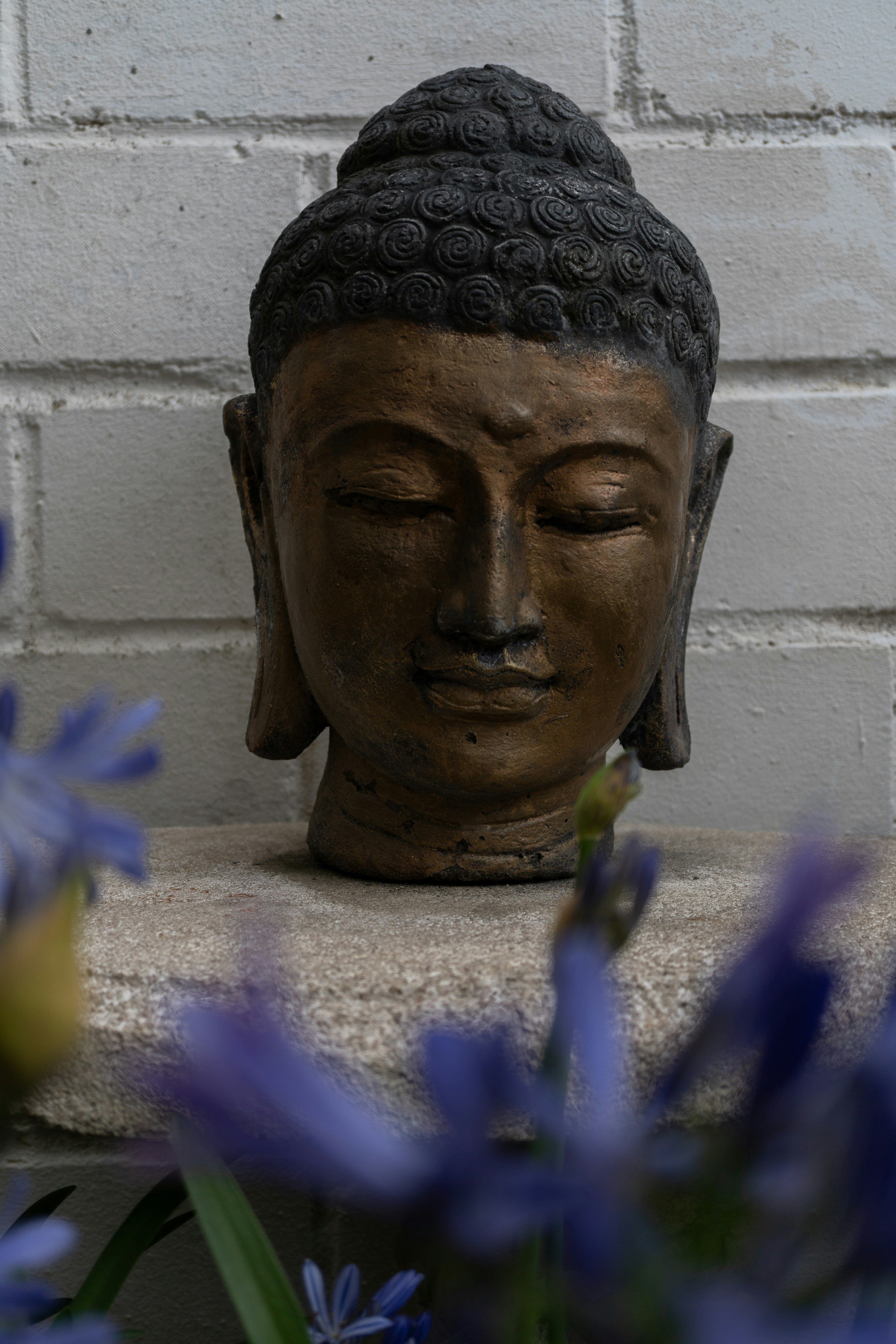 Tranquil Buddha Bust Amid Blurred Indigo Flowers