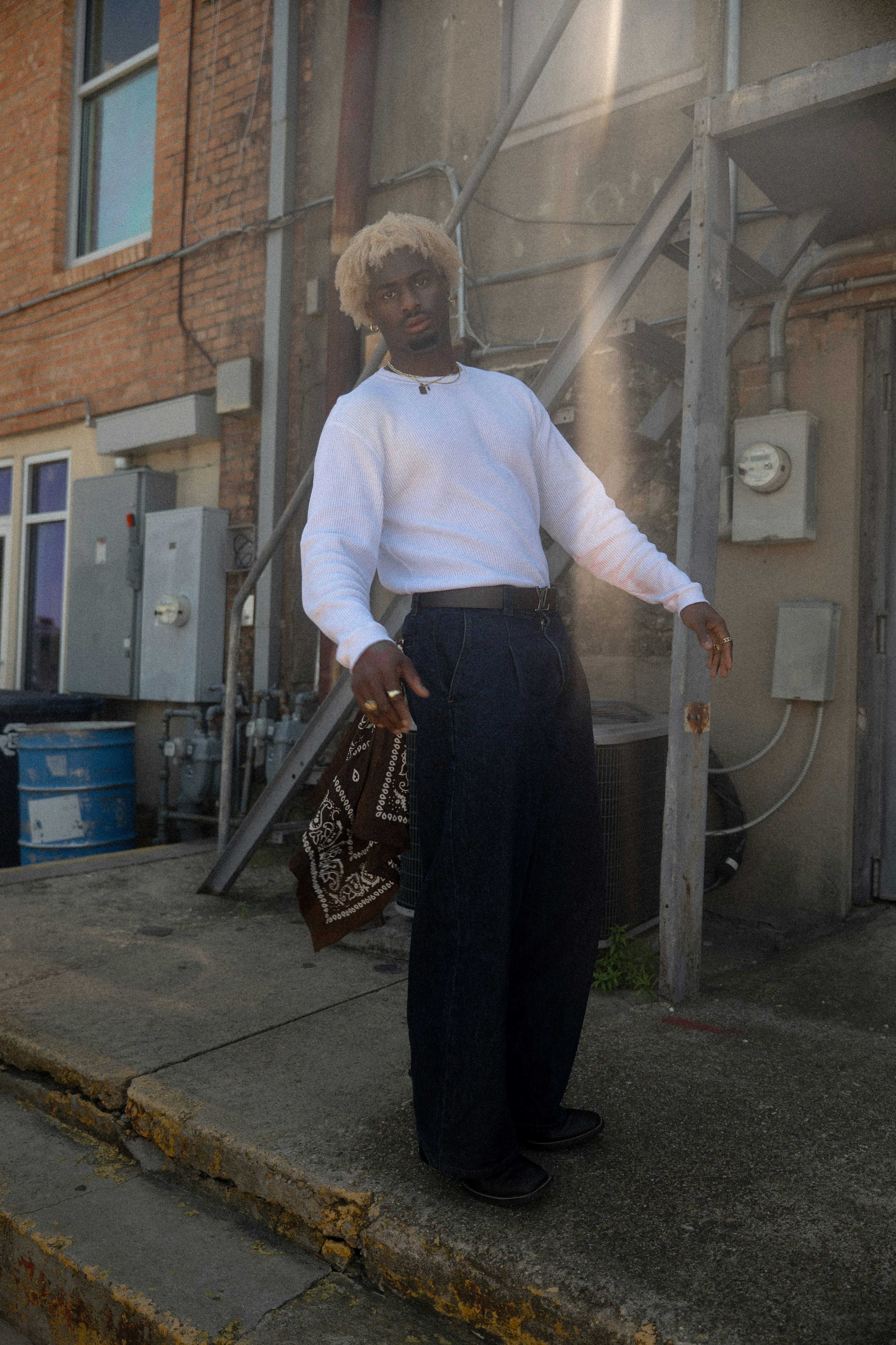 Urban portrait in a sunlit alleyway: a confident stance and bandana glimpse