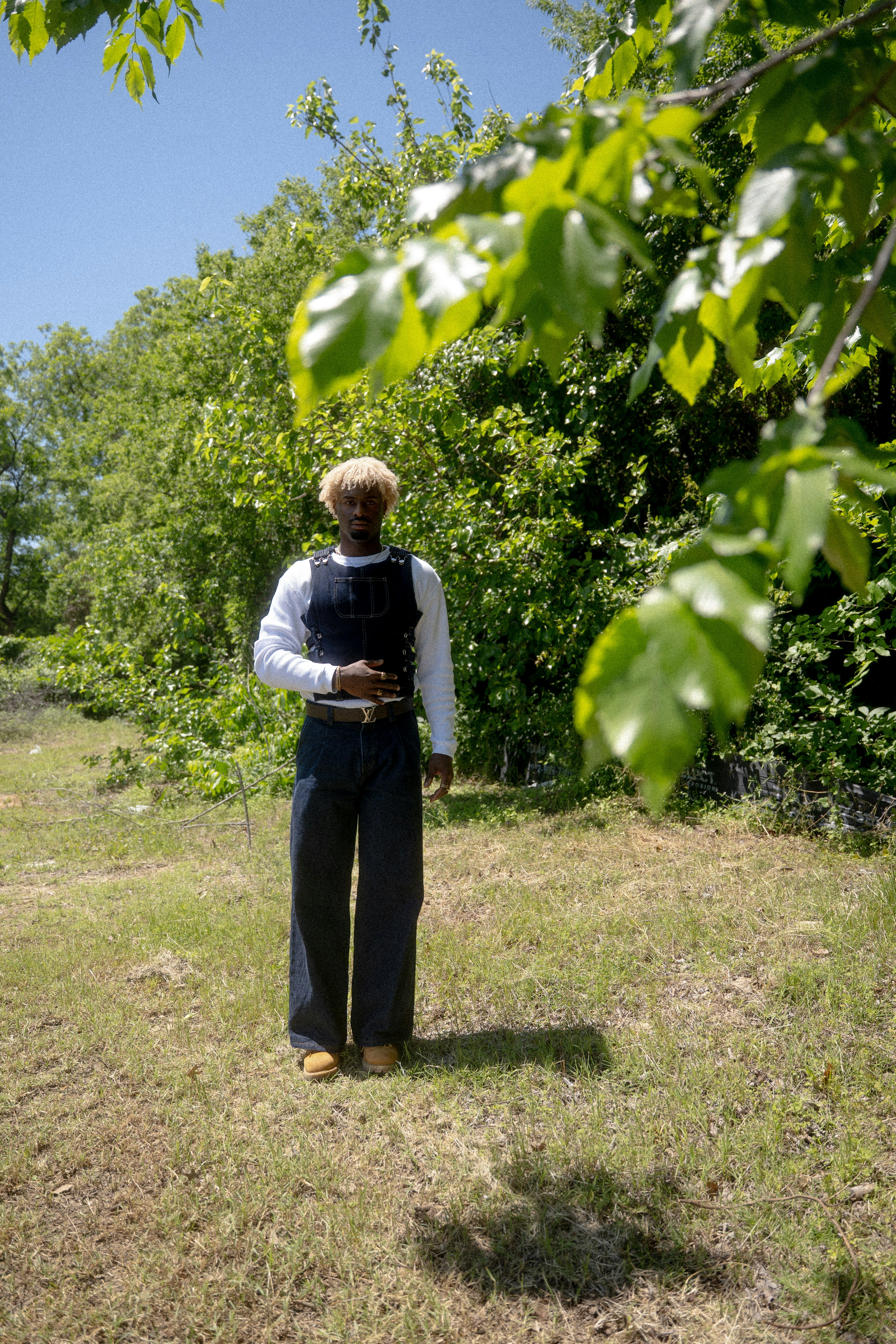 Young man in a sunlit orchard wearing a black vest amid green foliage