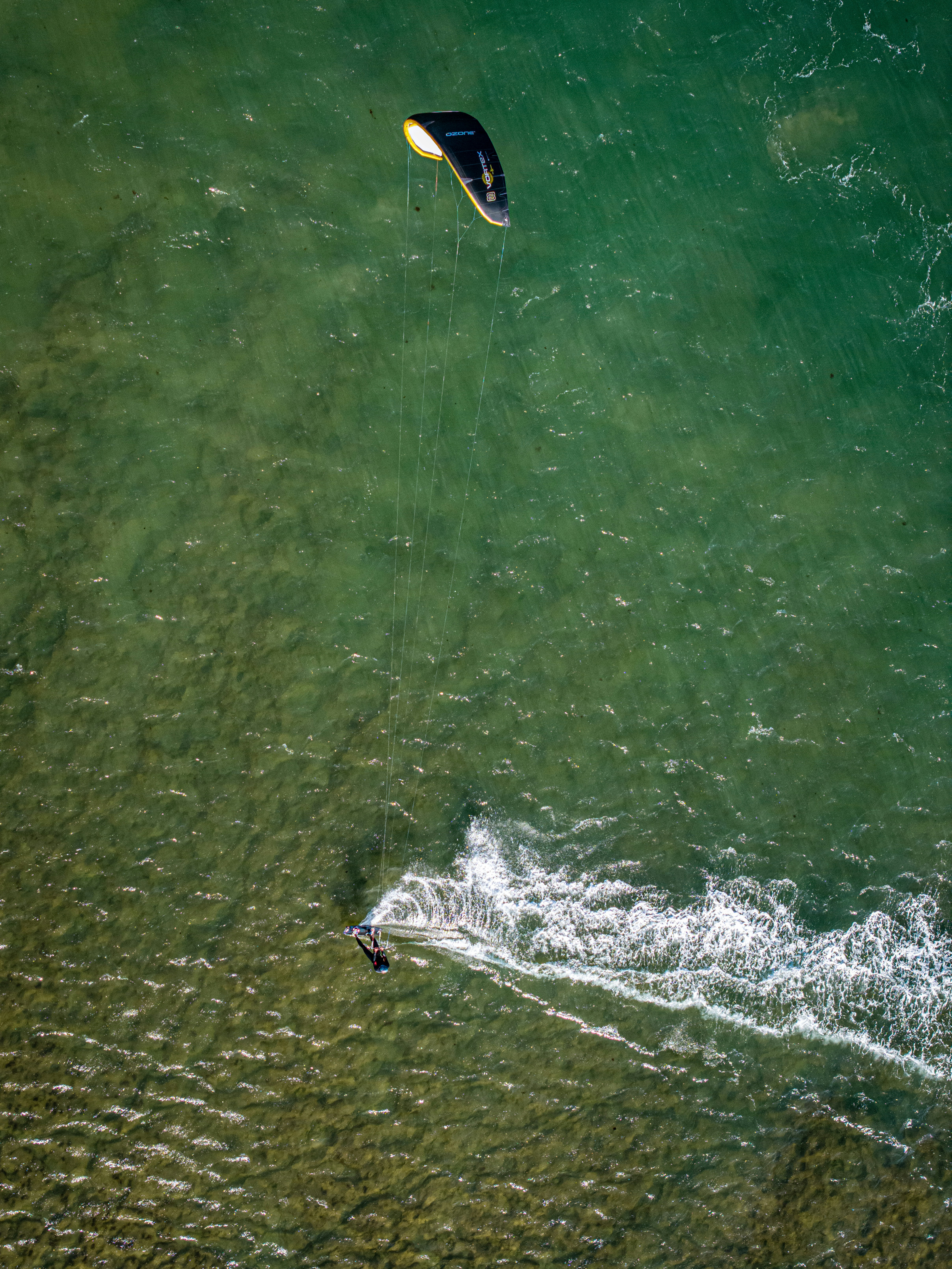 Soaring Silhouette: A Kite Surfer Traces a Wake from Above