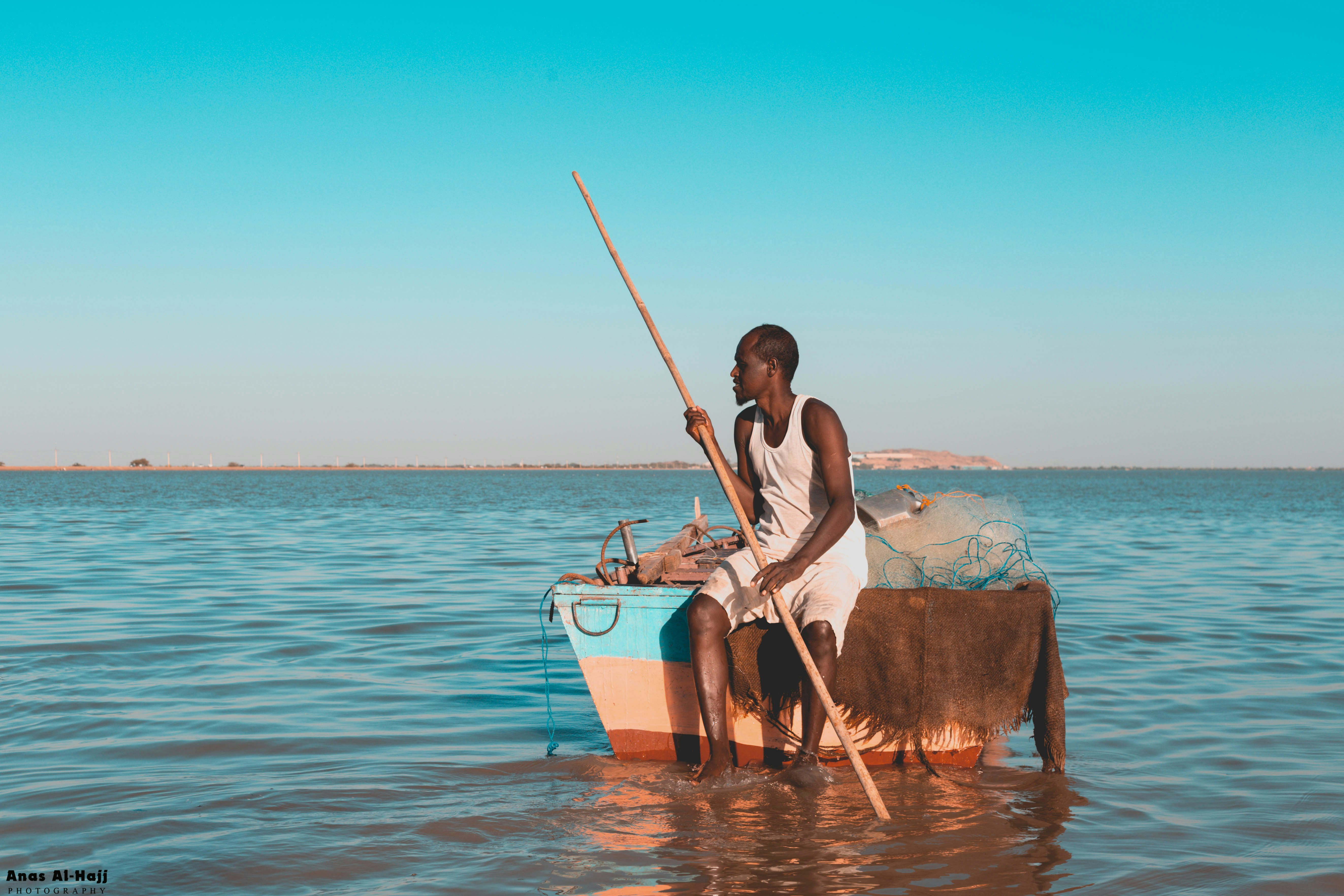 Horizon hunter: a lone fisherman navigating calm waters with a long pole