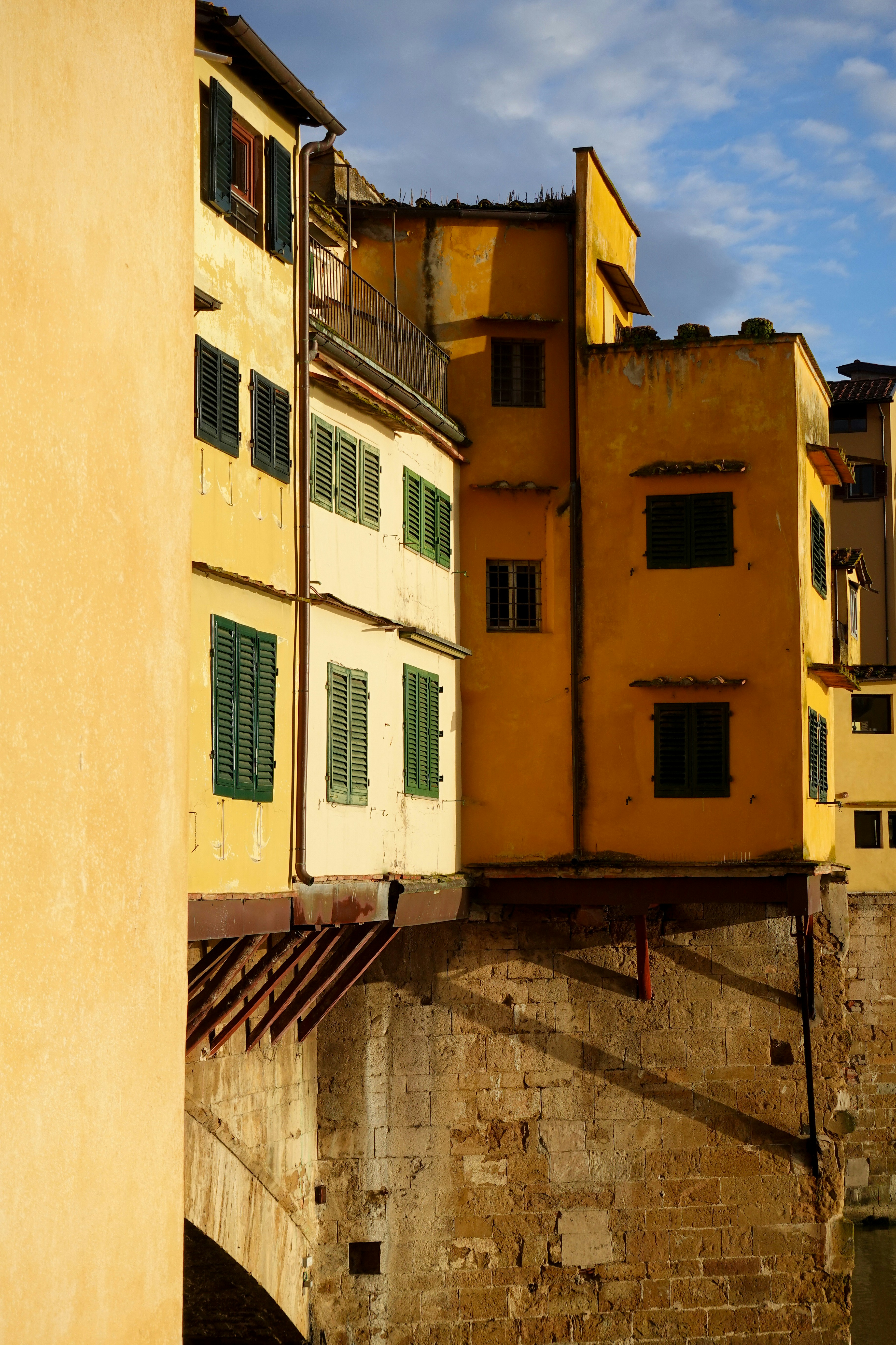 Yellow buildings with green shutters over a stone bridge.
