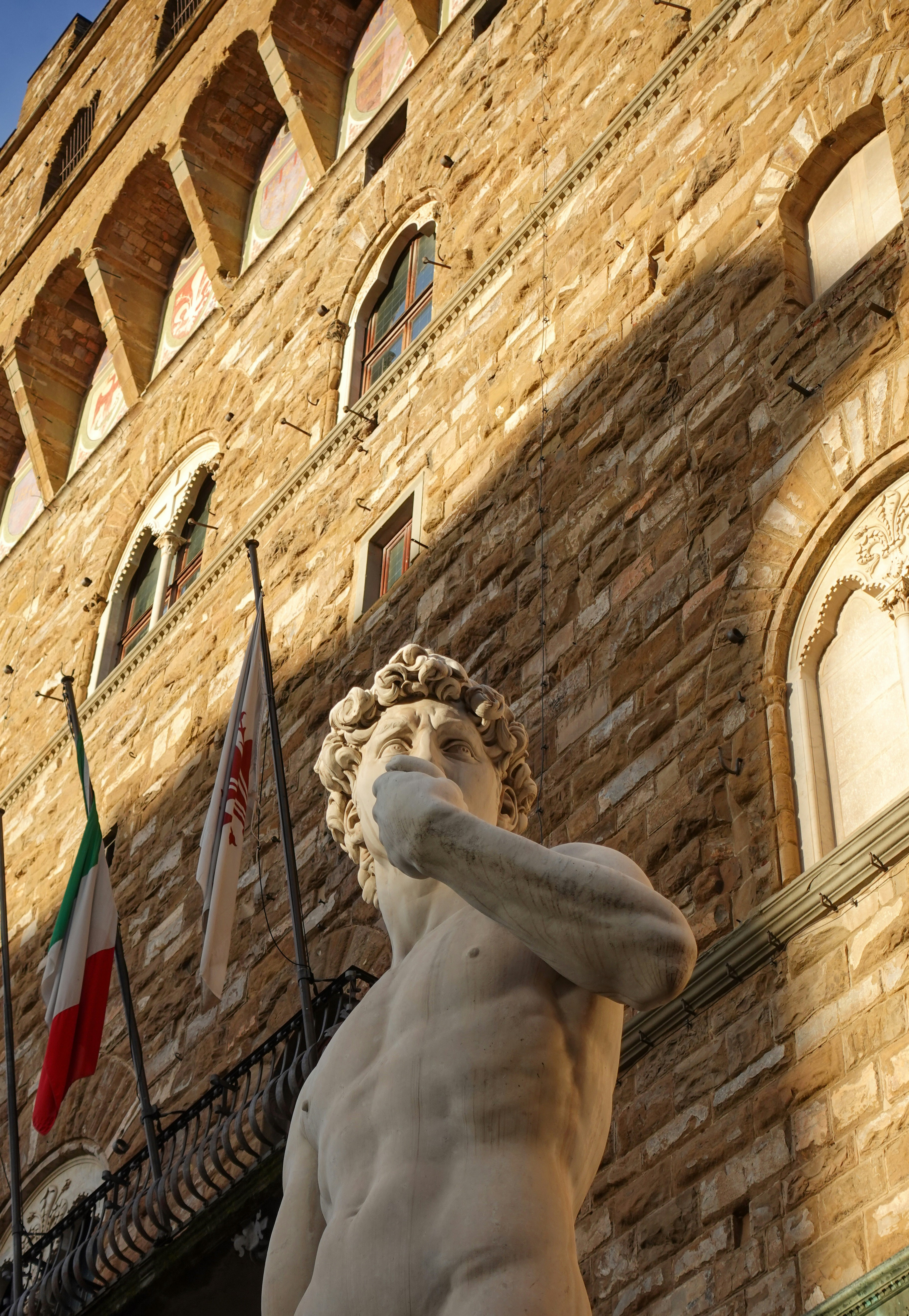 Statue Against Stony Facade: A Moment Beneath the Italian Flags
