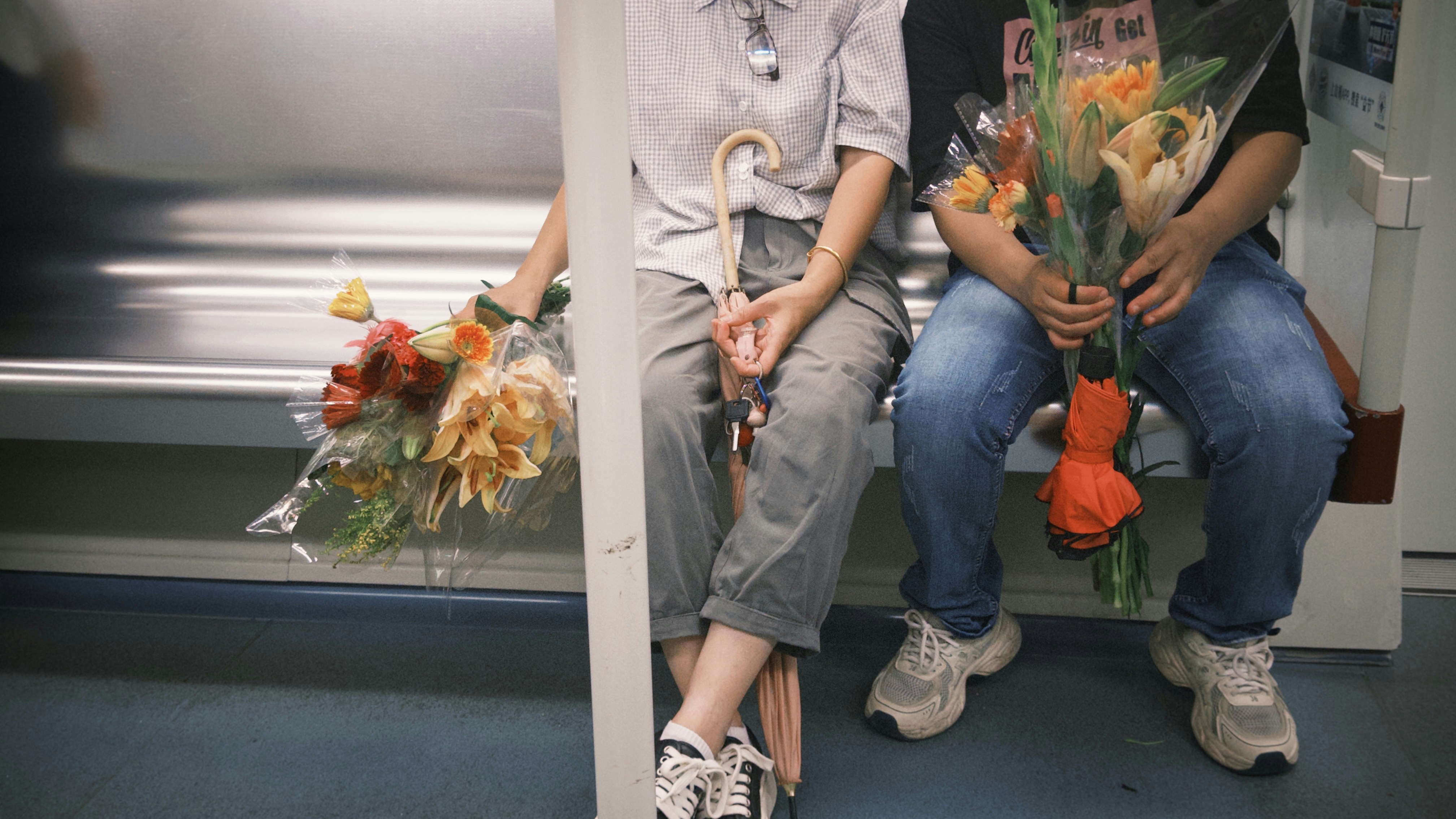 Two commuters with bouquets sharing a moment on a subway bench