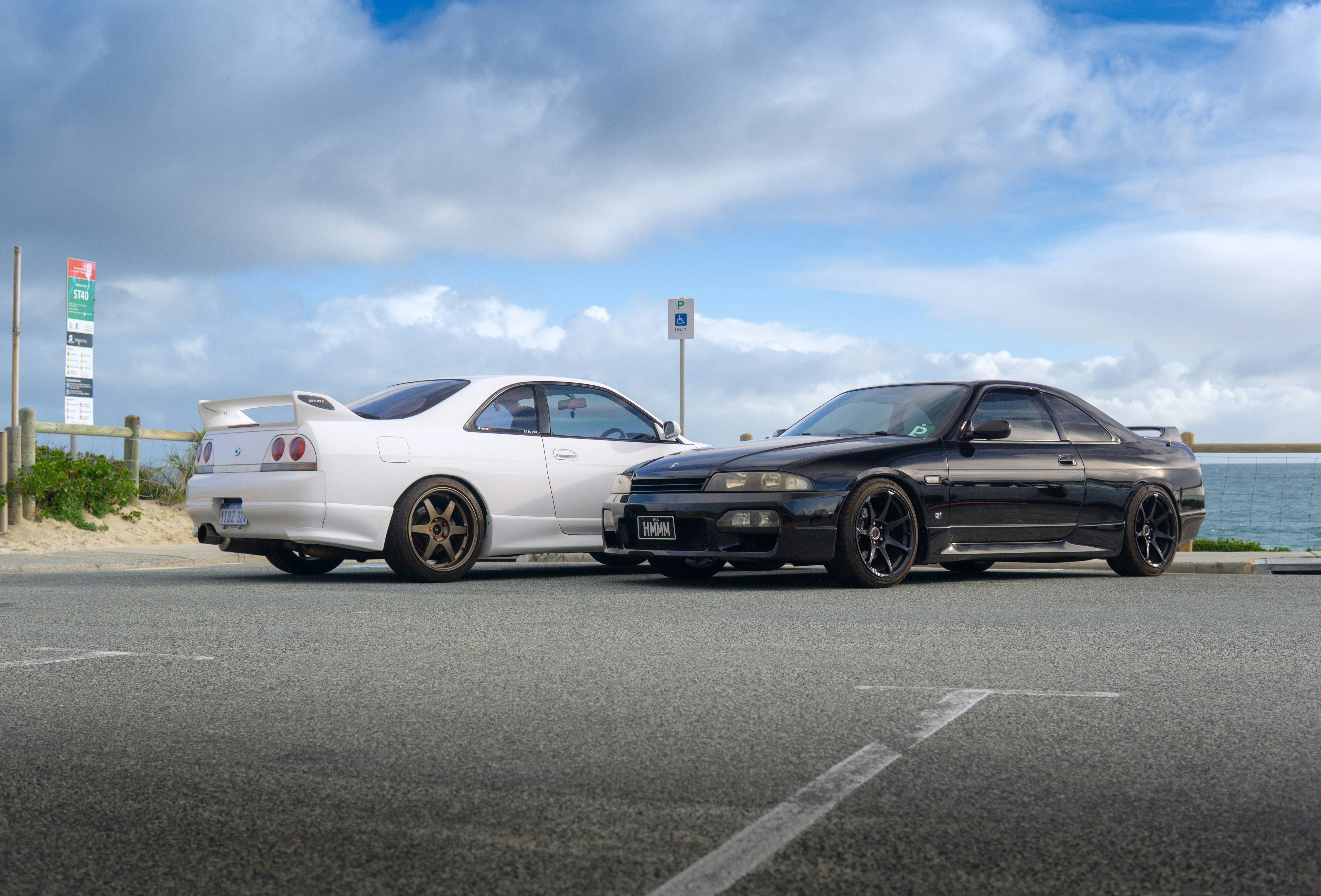 Twin-Stance by the Sea: White and Black Settee Cars Meet the Ocean