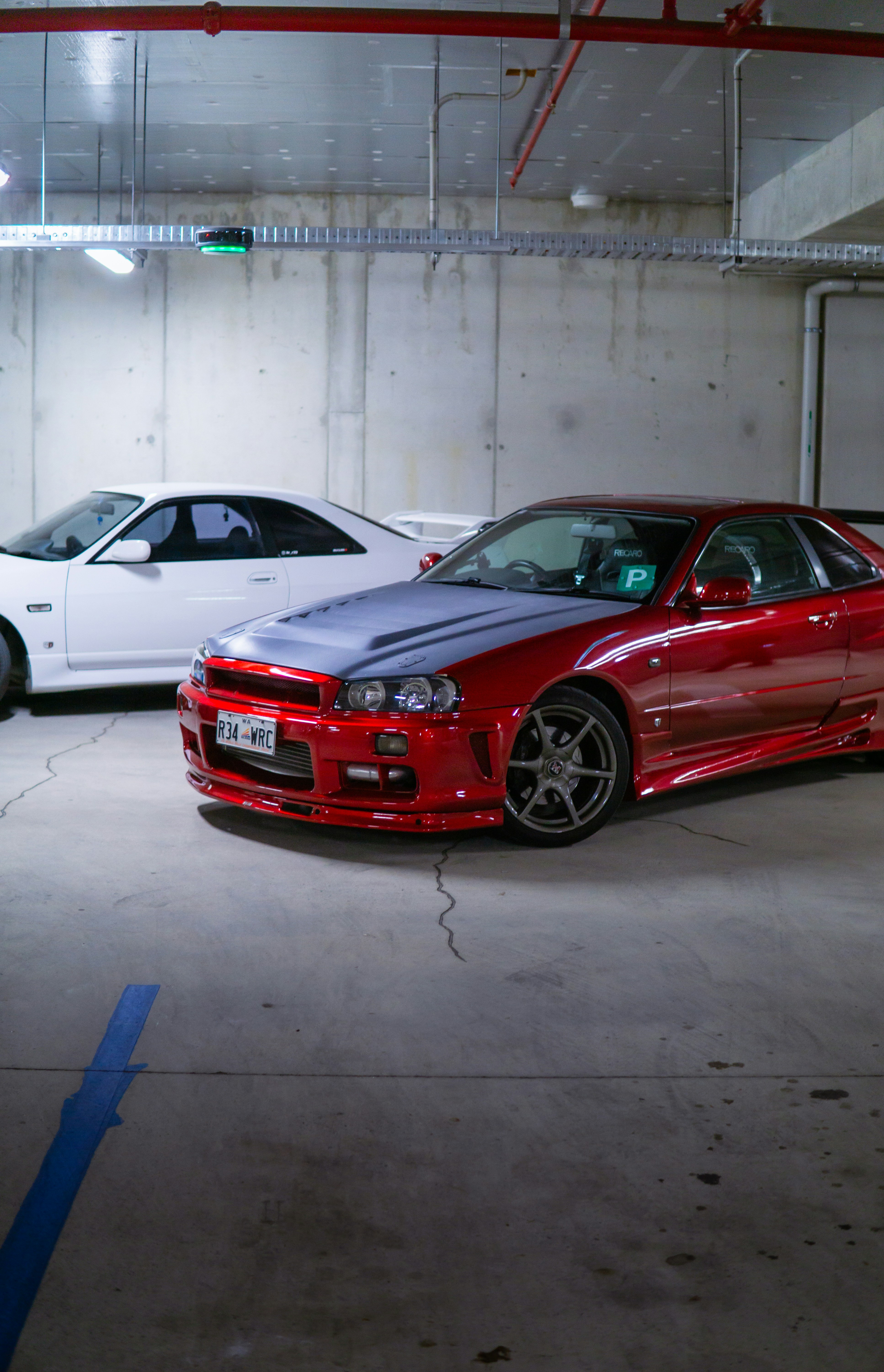 Red Nissan Skyline gleams under concrete ceiling in a dim parking level