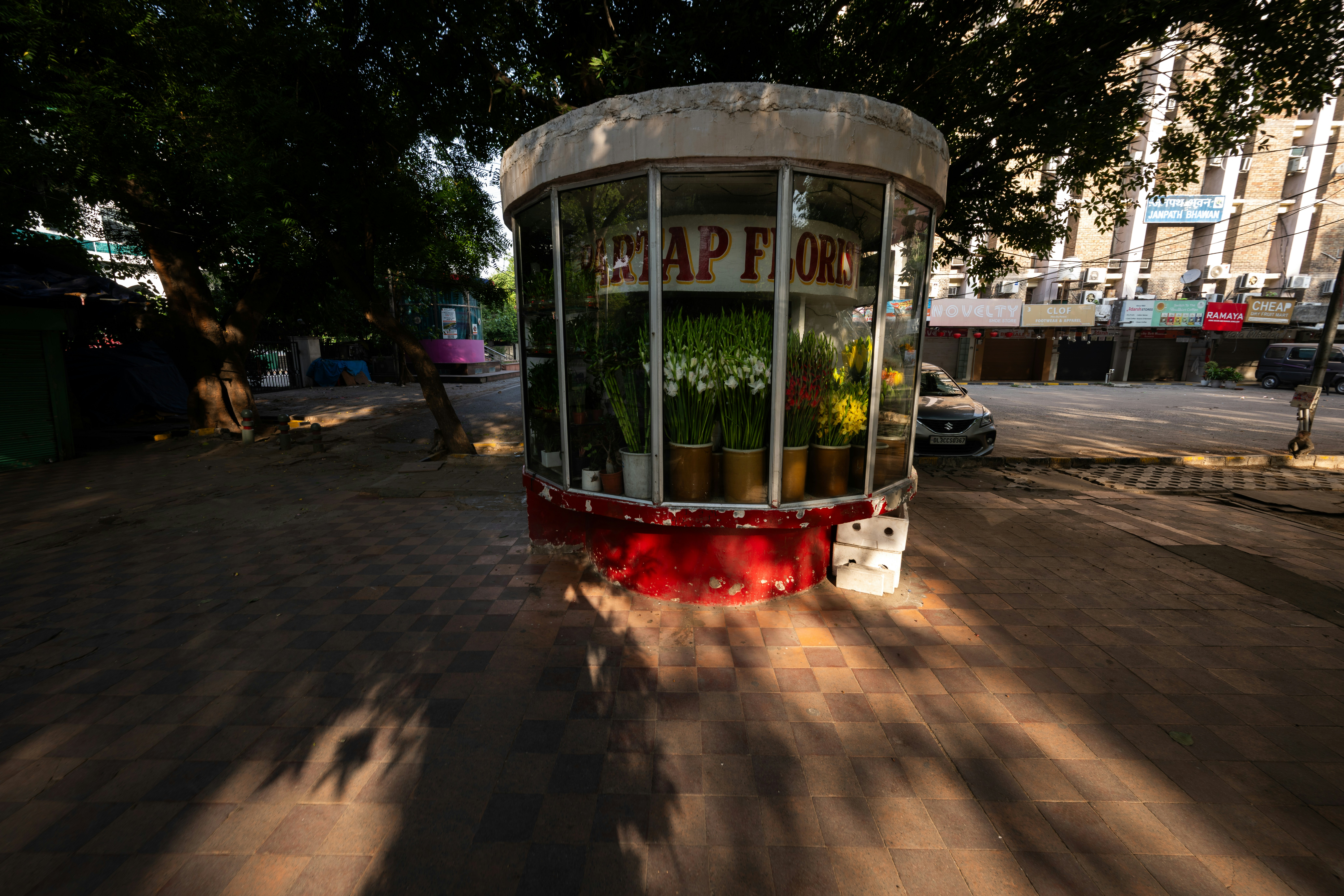 Glass kiosk with potted plants on sunlit plaza