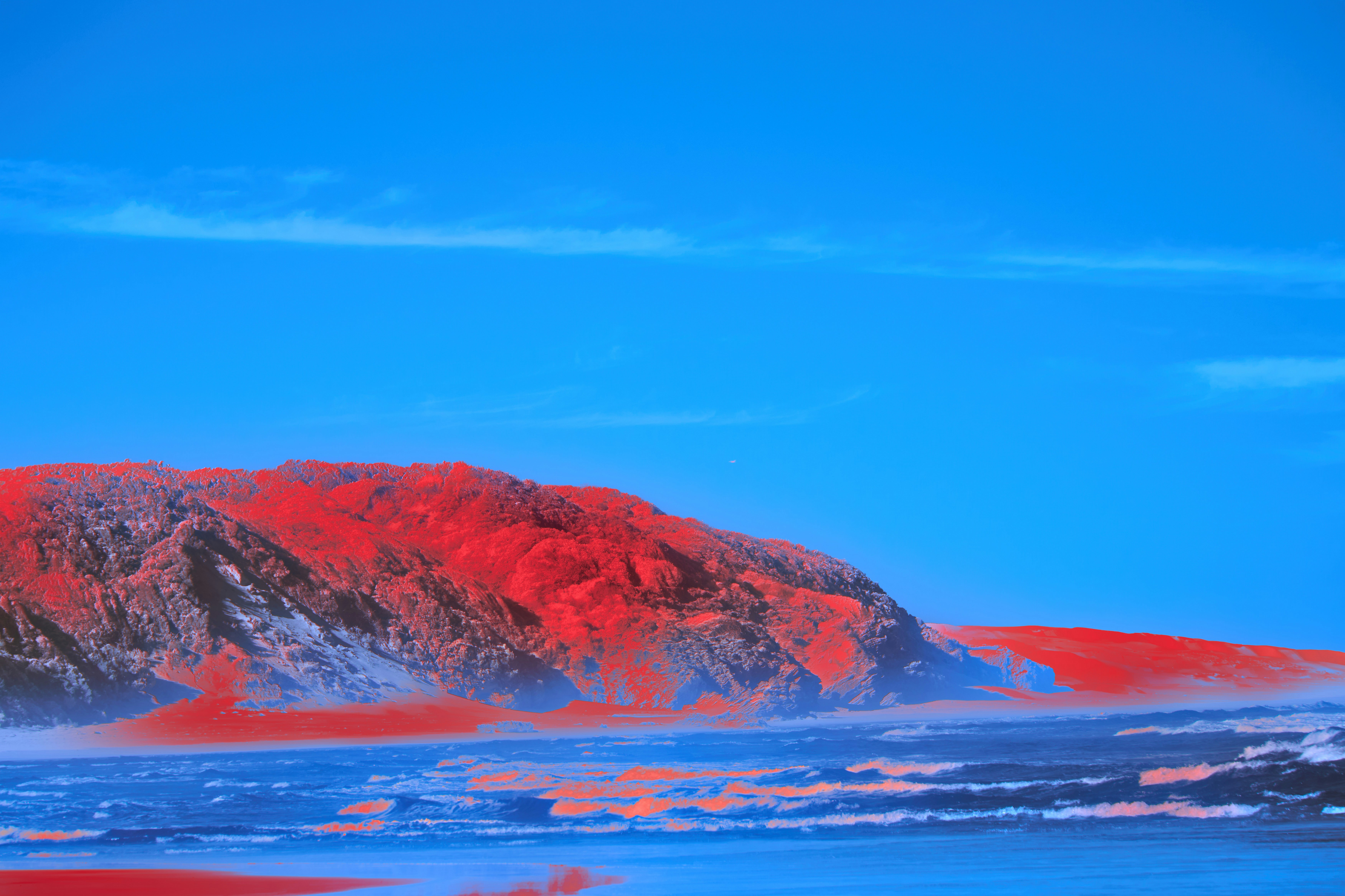Red-cliffed coastline beneath a cerulean sky, with icy shoreline accents