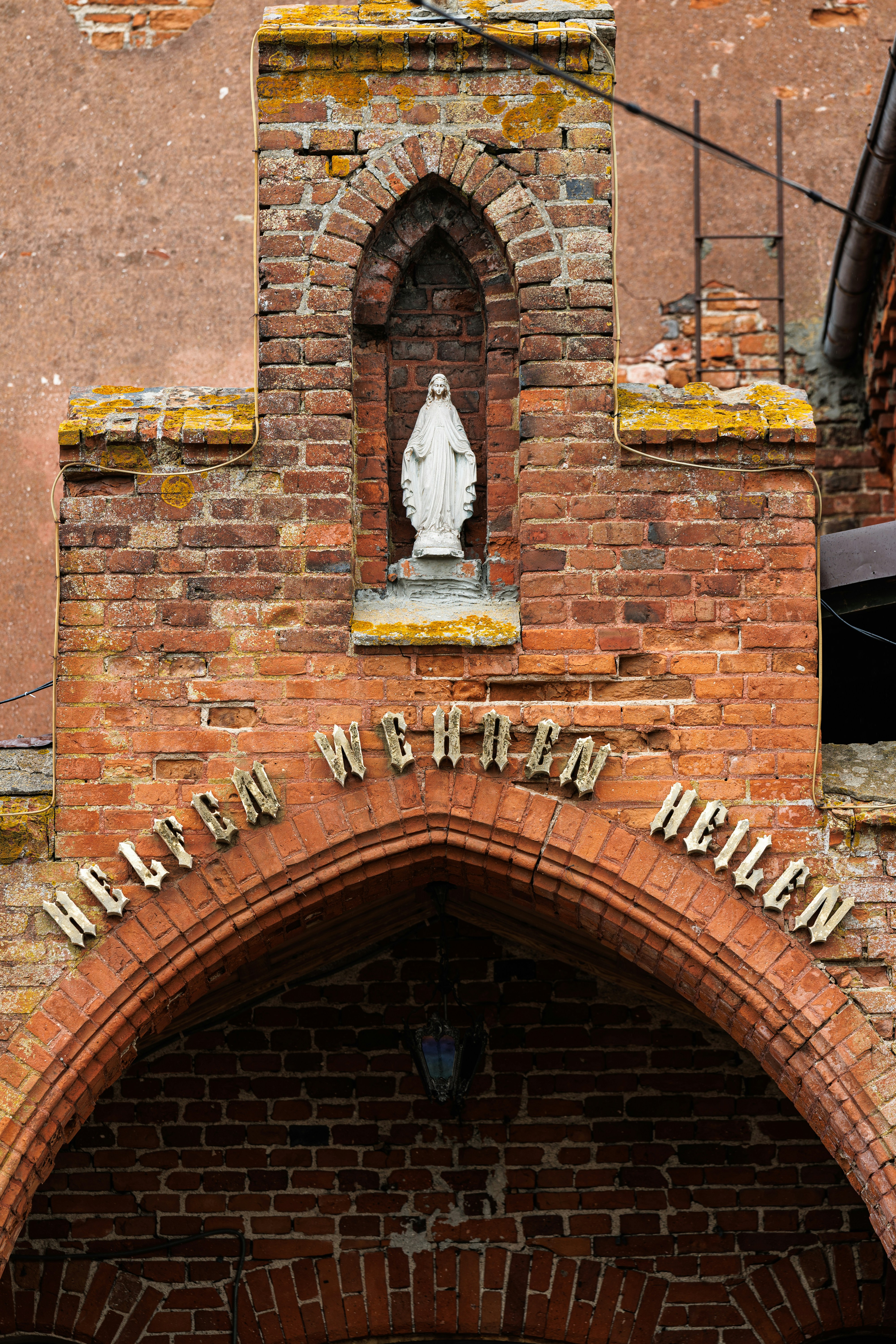Statue in a Brick Arch: A Weathered Chapel Above the Archway