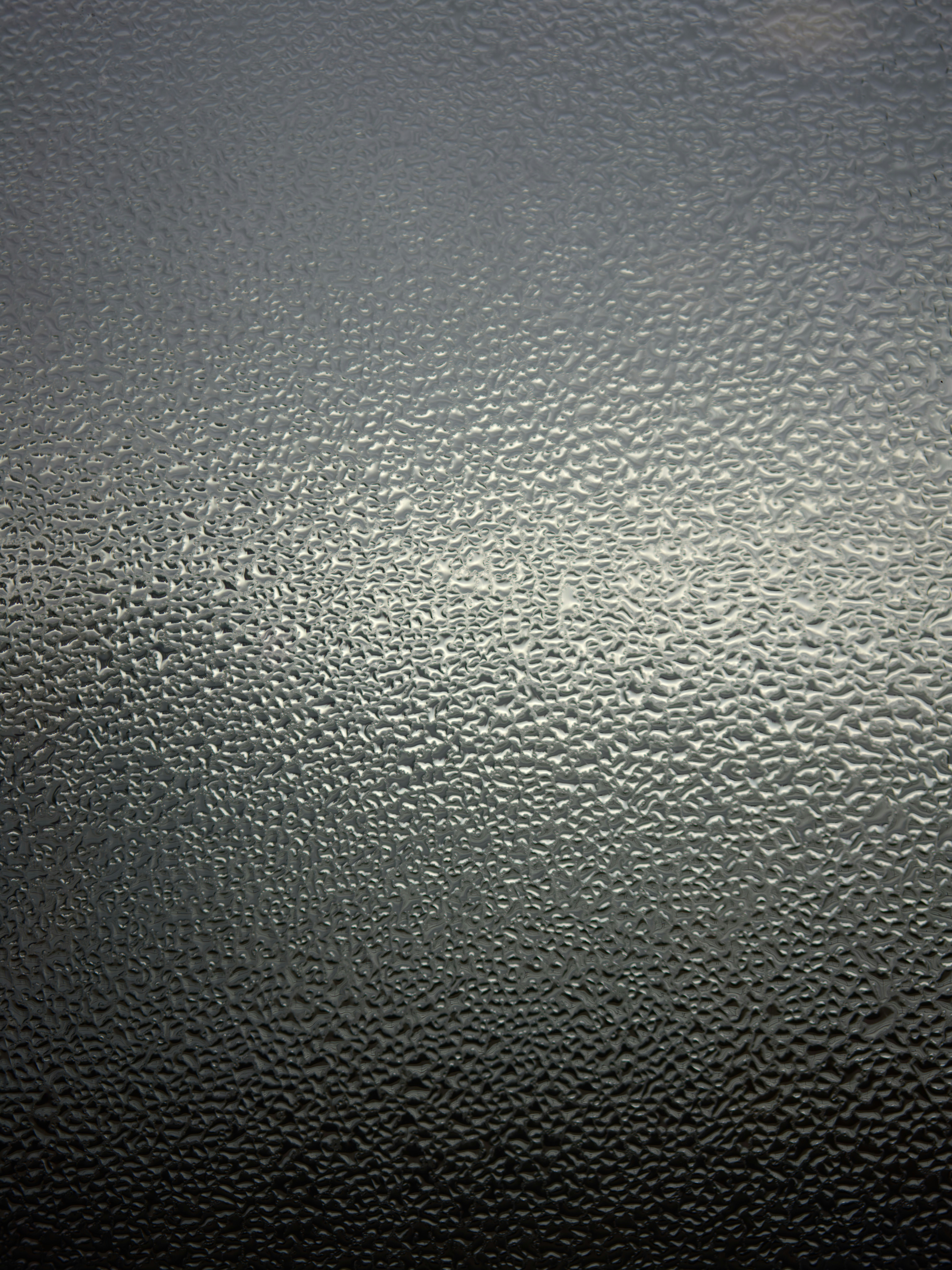 Condensation forming across a window after the rain, turning the glass into a textured, abstract surface. The soft gradient of light behind the fogged glass creates a quiet atmosphere suspended between weather, temperature, and silence.