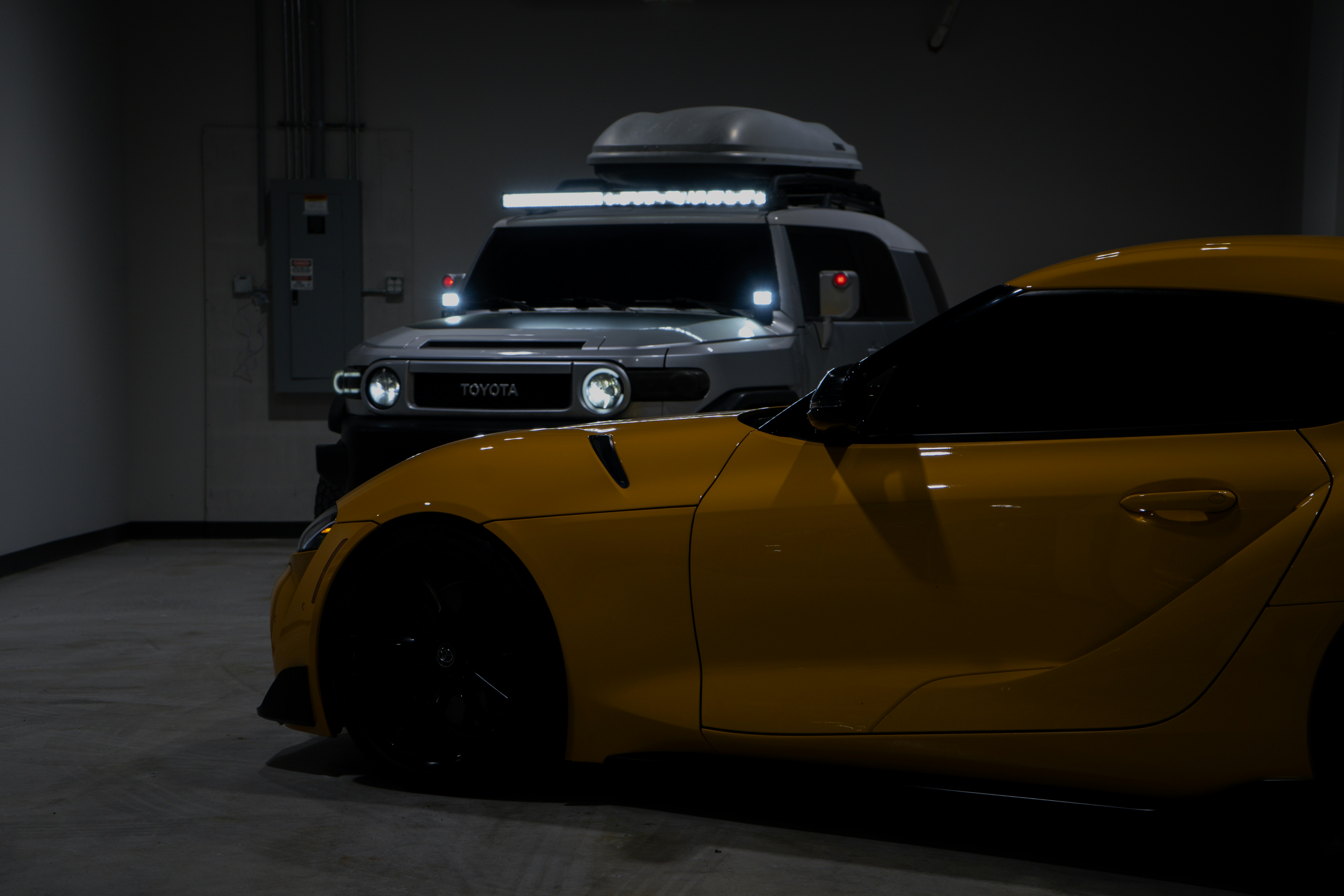Yellow sports car in shadowed garage with a rugged off-road vehicle behind