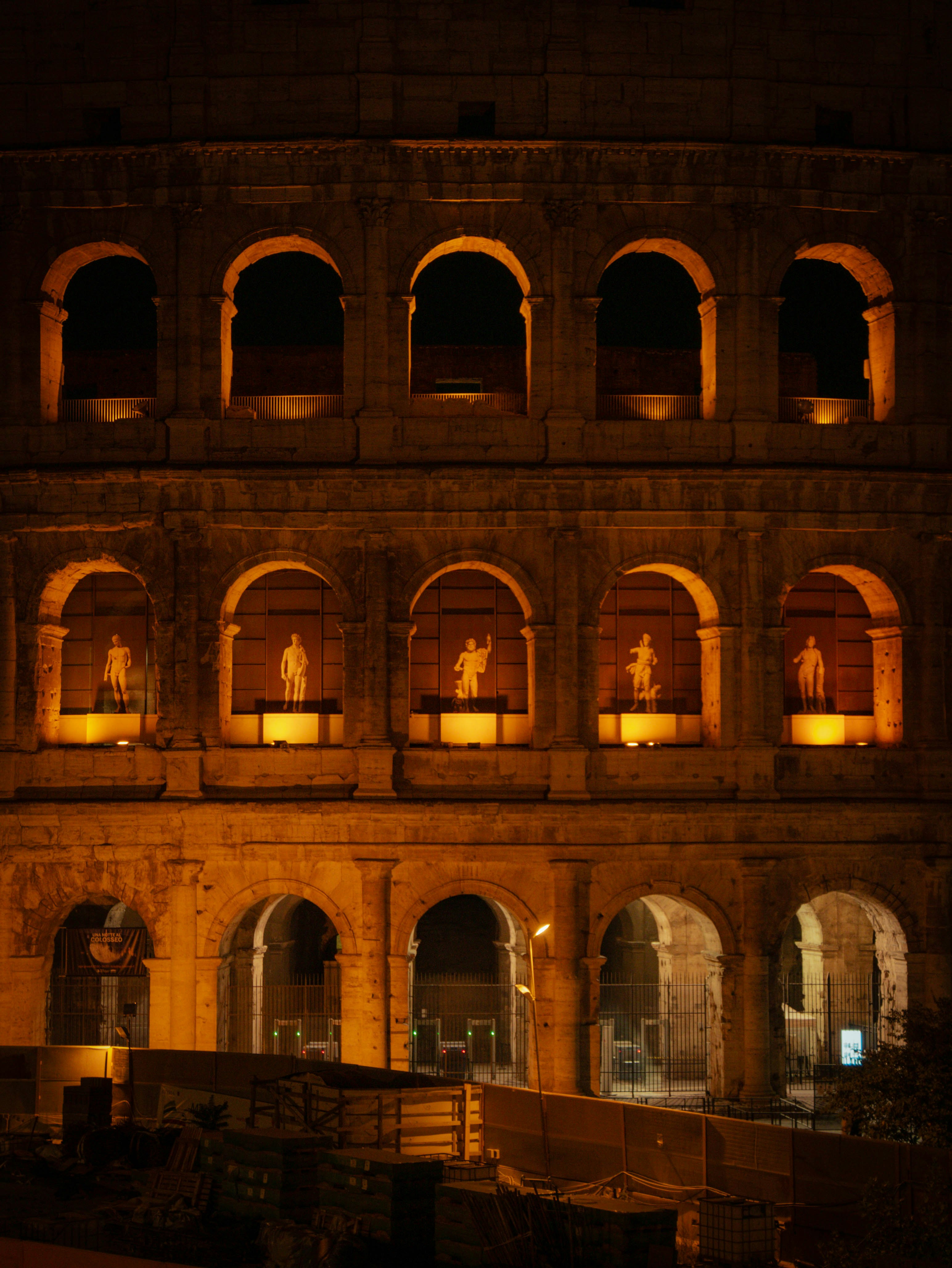 The illuminated colosseum at night with statues in its arches.