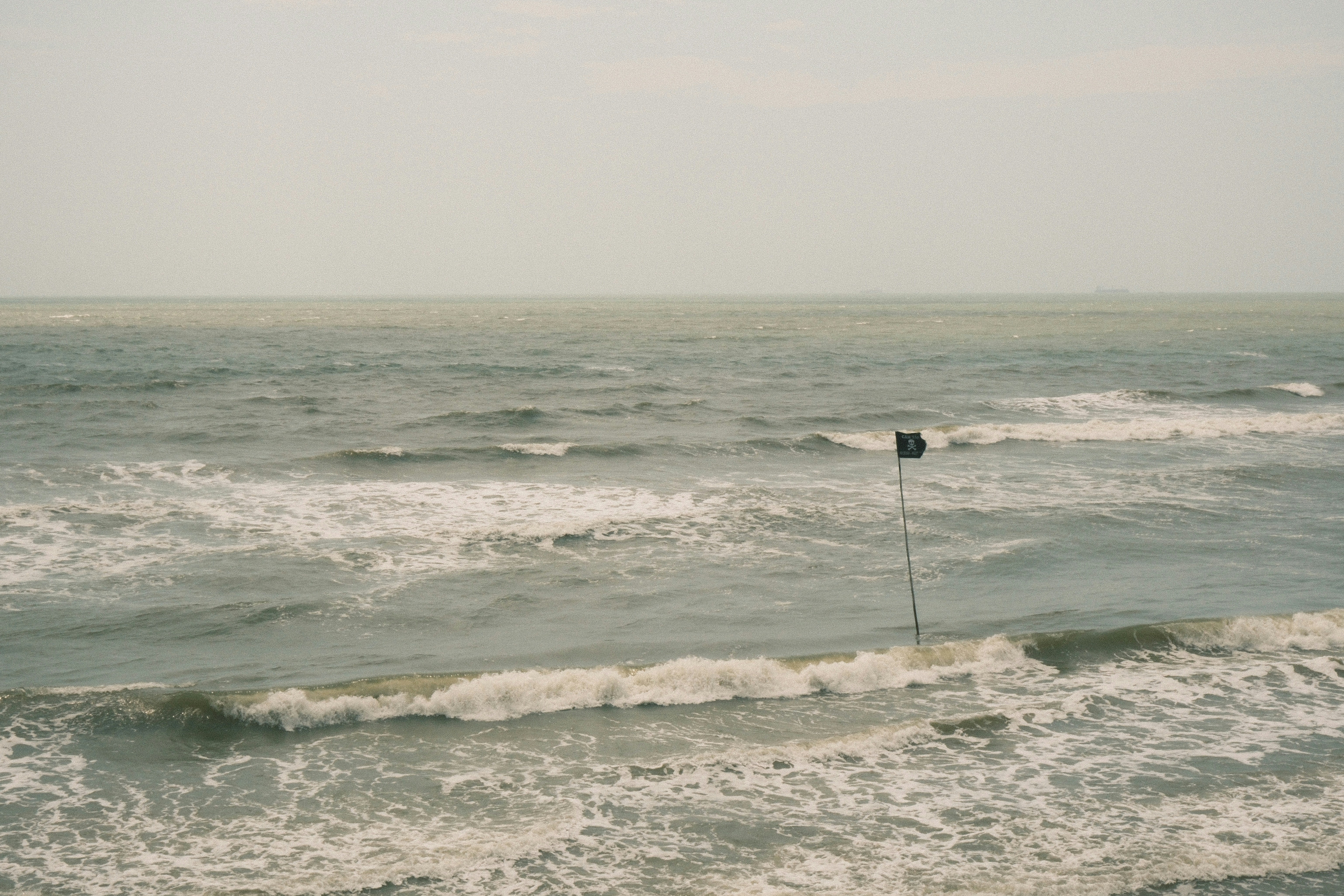 Flag in the Sea: A Lone Marker Amid Rolling Coastal Waves