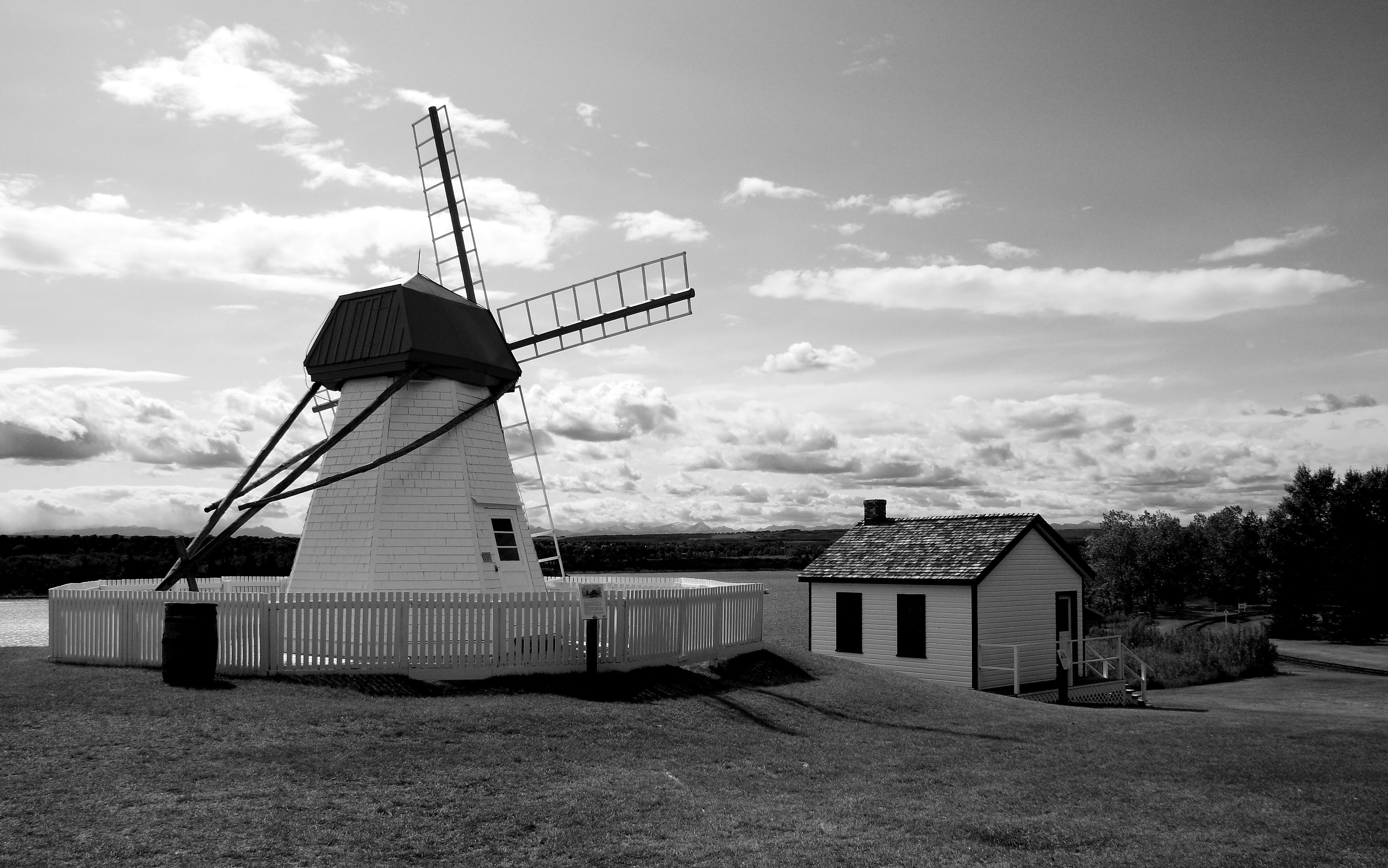 Black and white windmill and house under a cloudy sky.