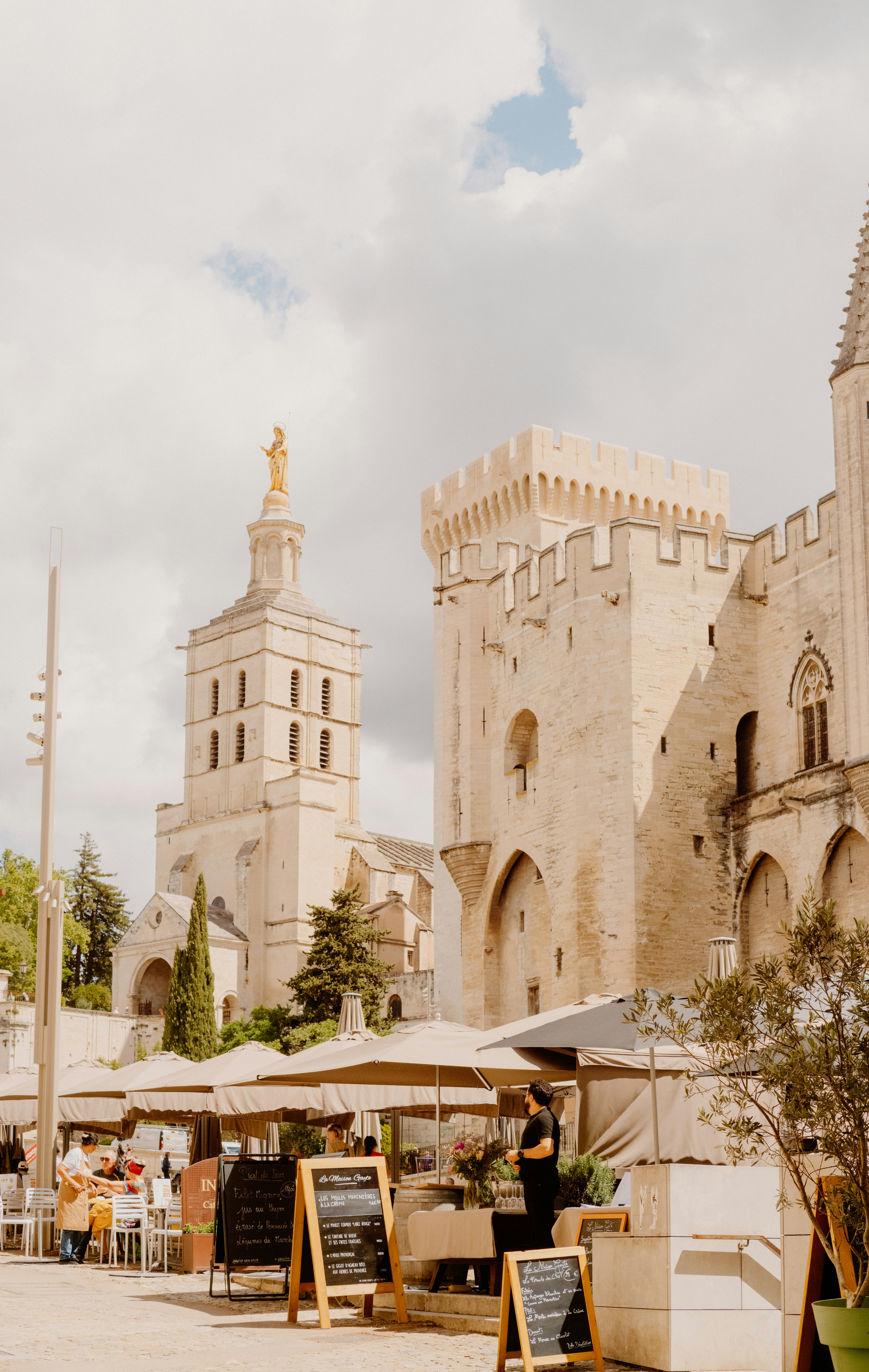 A sunlit plaza beside ancient stone arches and a stately tower