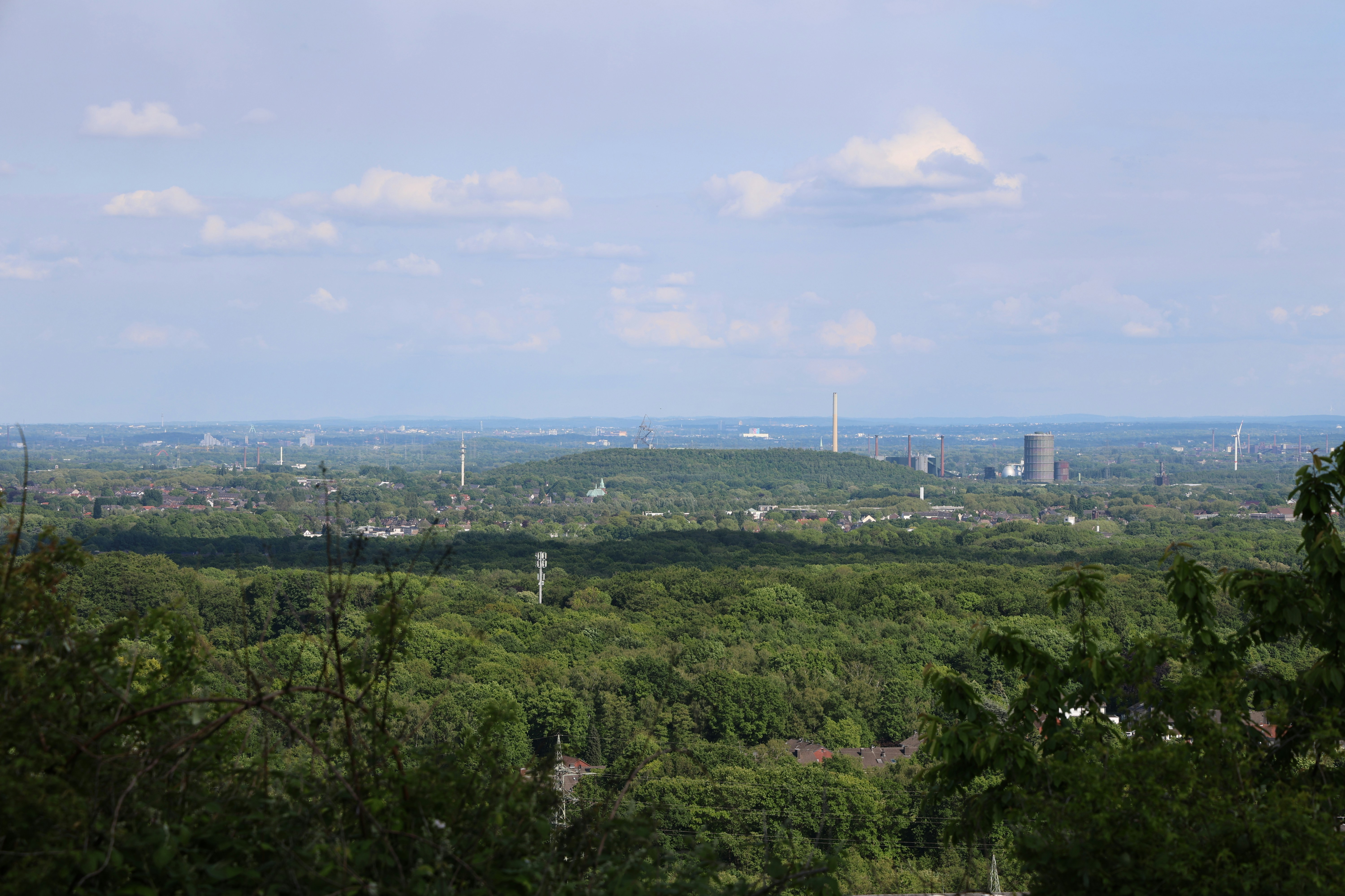 Vast Green Horizon: Industrial Silhouettes Above a Forested Valley