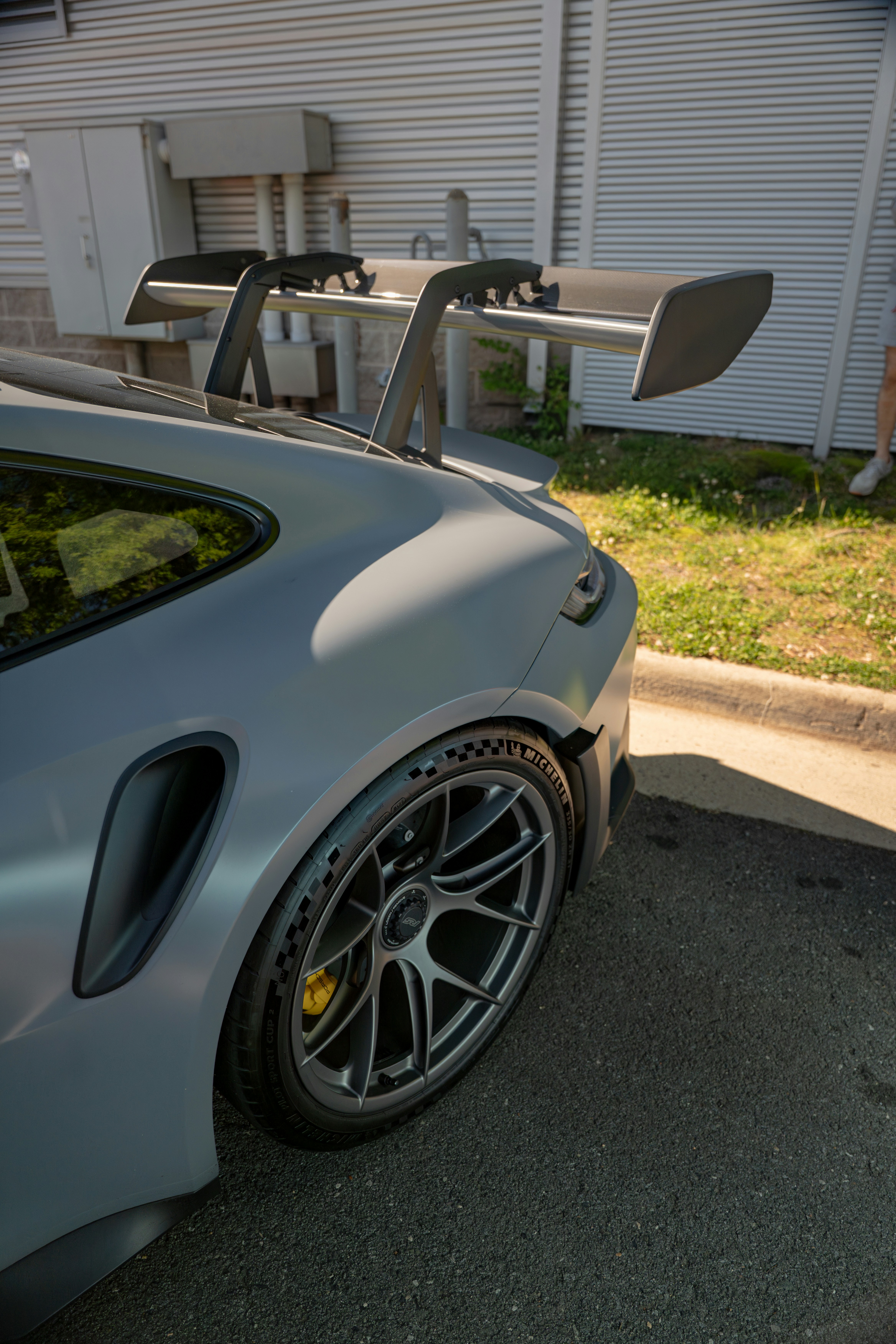 Rear Wing and Tire Detail of a Silver Porsche in Sunlit Parking