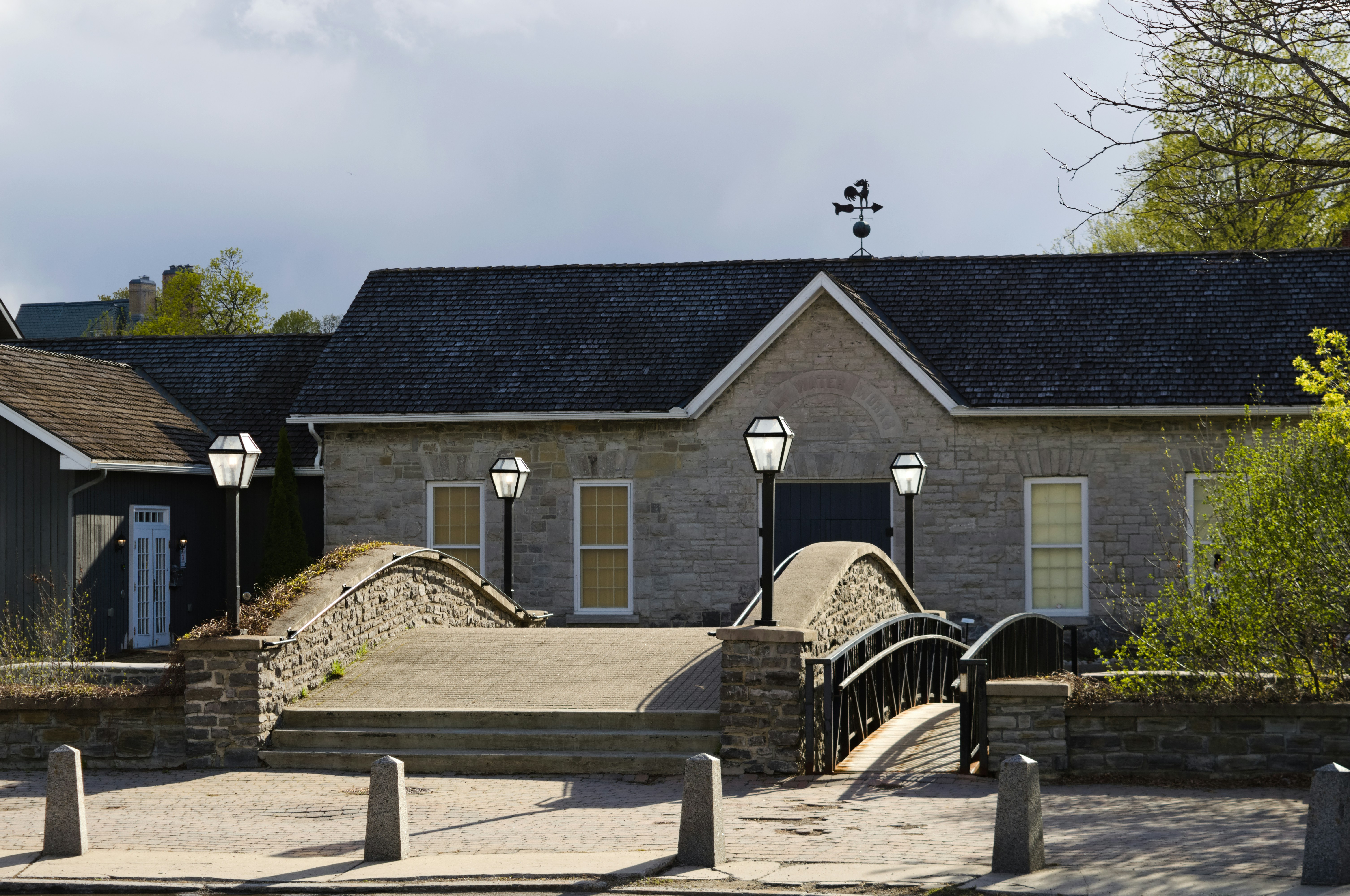 Stone-arched riverside bridge leading to a quiet brick-clad pavilion