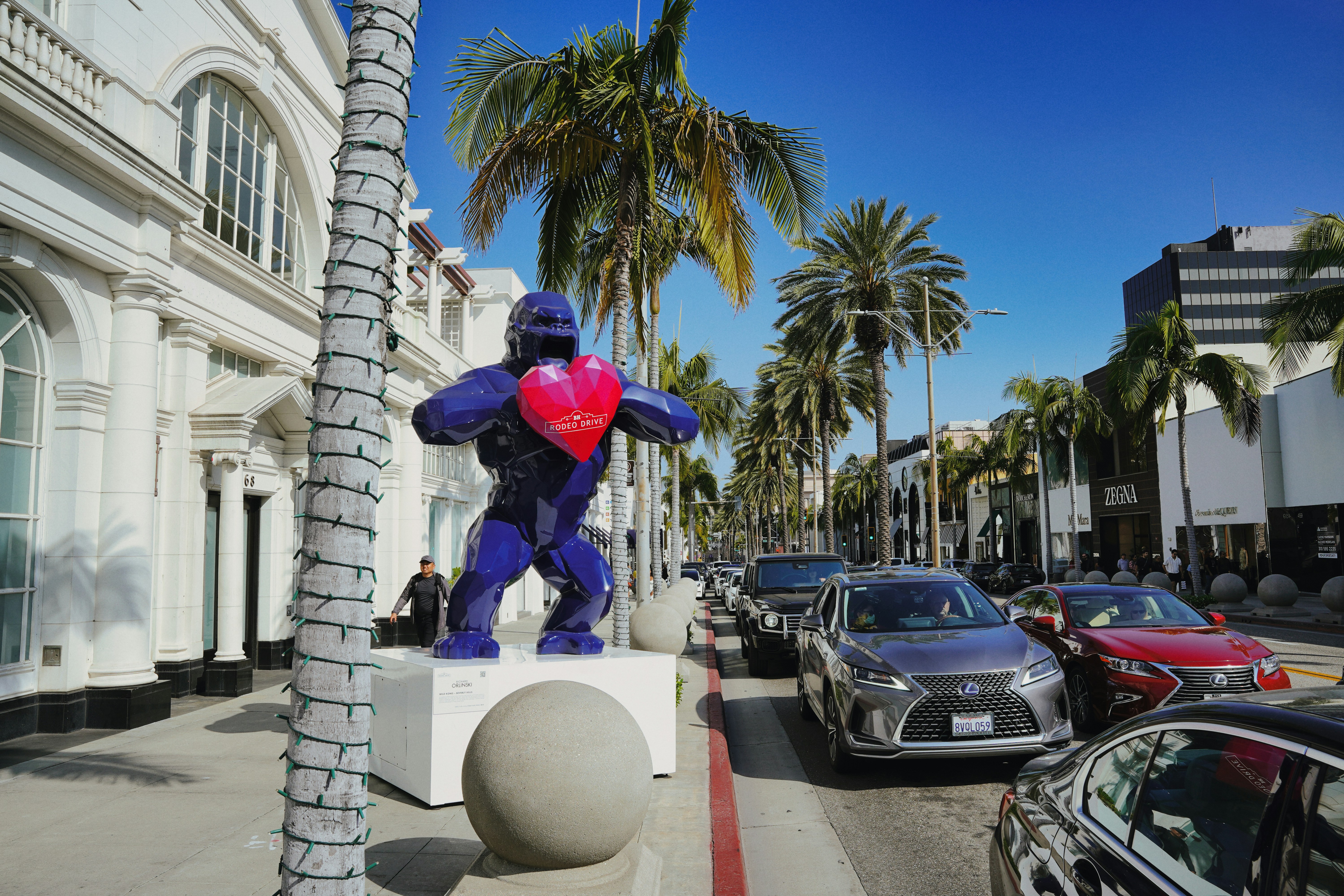 Giant purple heart-armed sculpture guarding a sunlit boulevard