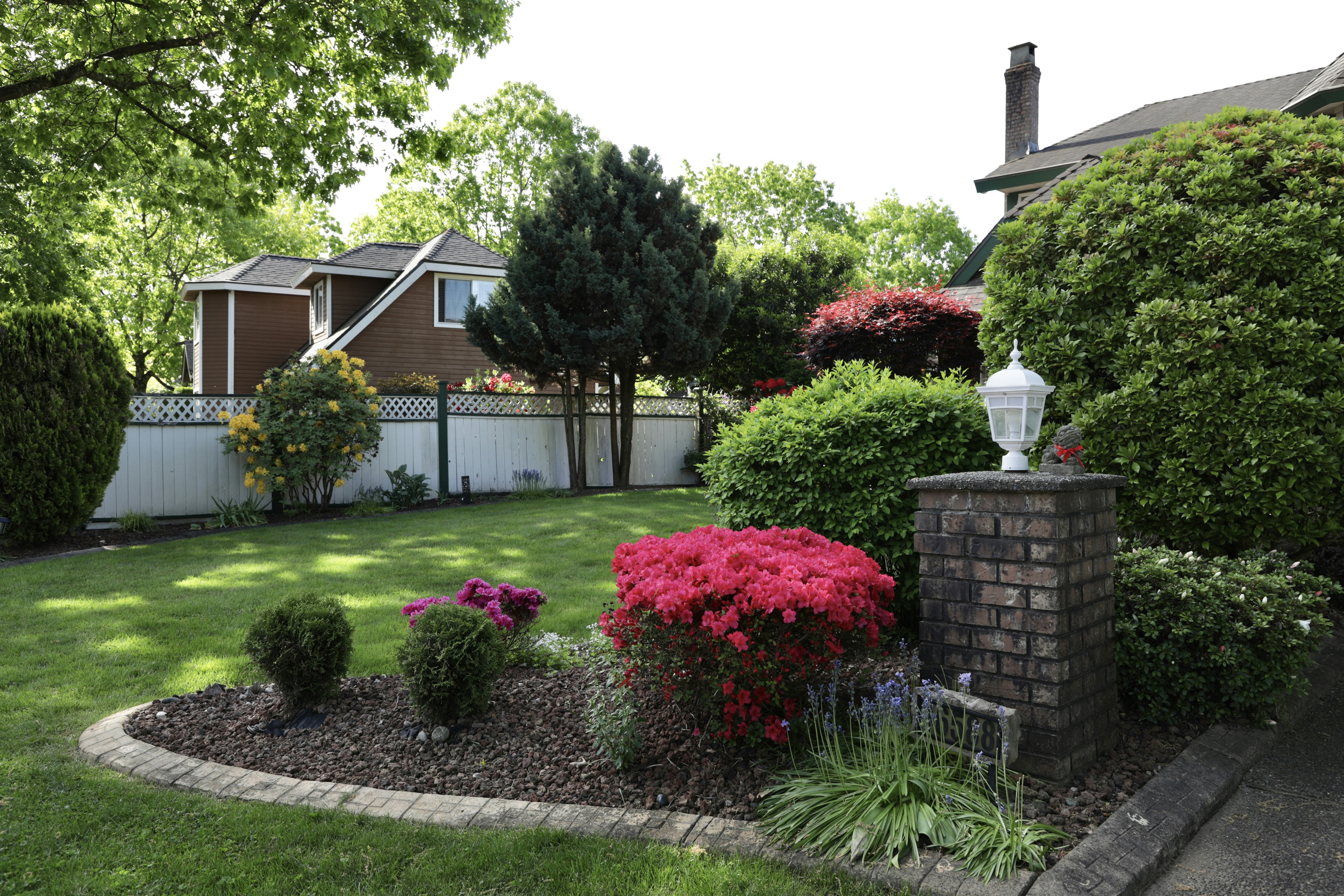 Neatly manicured front yard with vibrant azalea and lantern-lit pillar