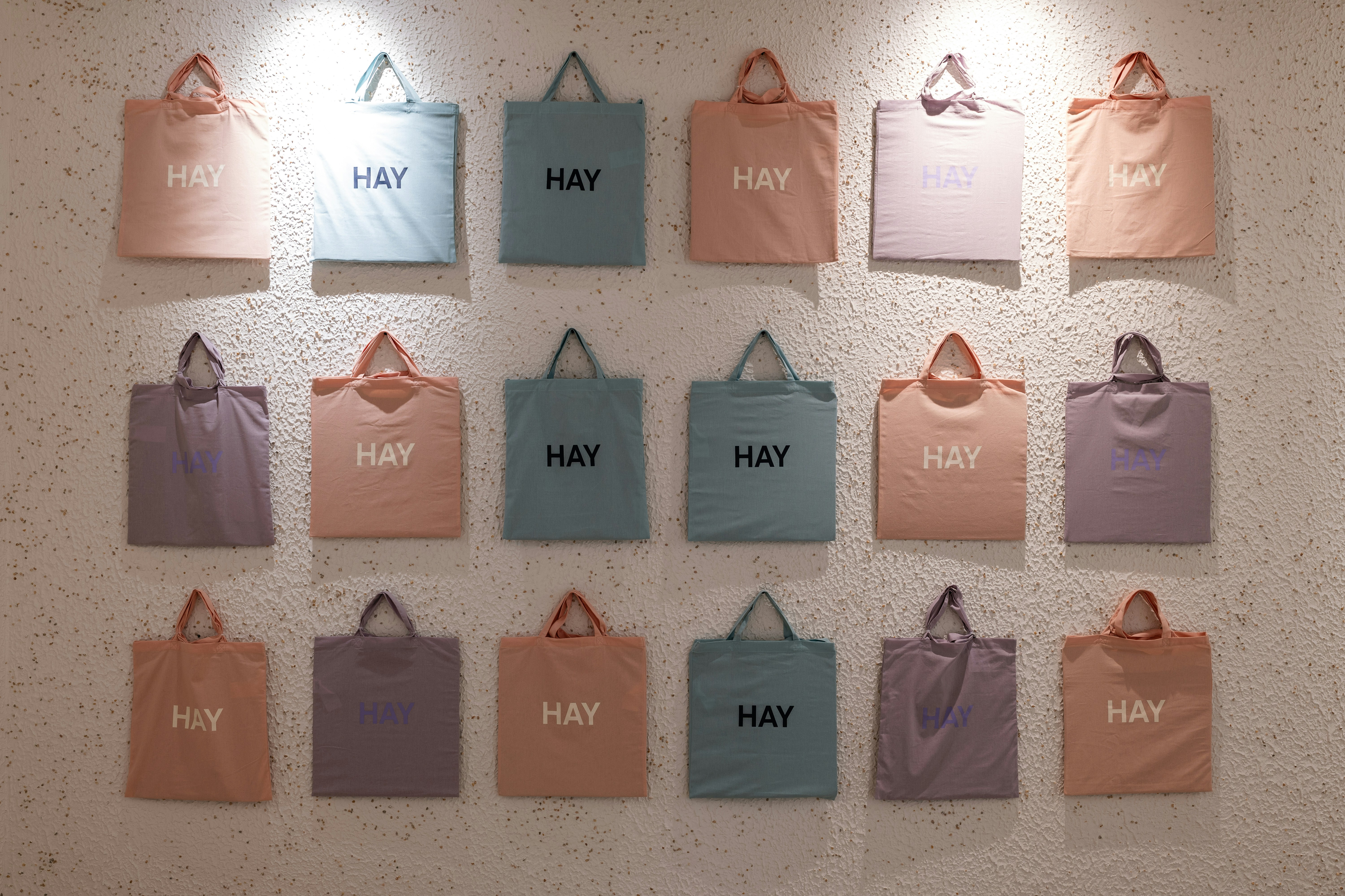Array of pastels: a grid of reusable shopping bags on a speckled wall