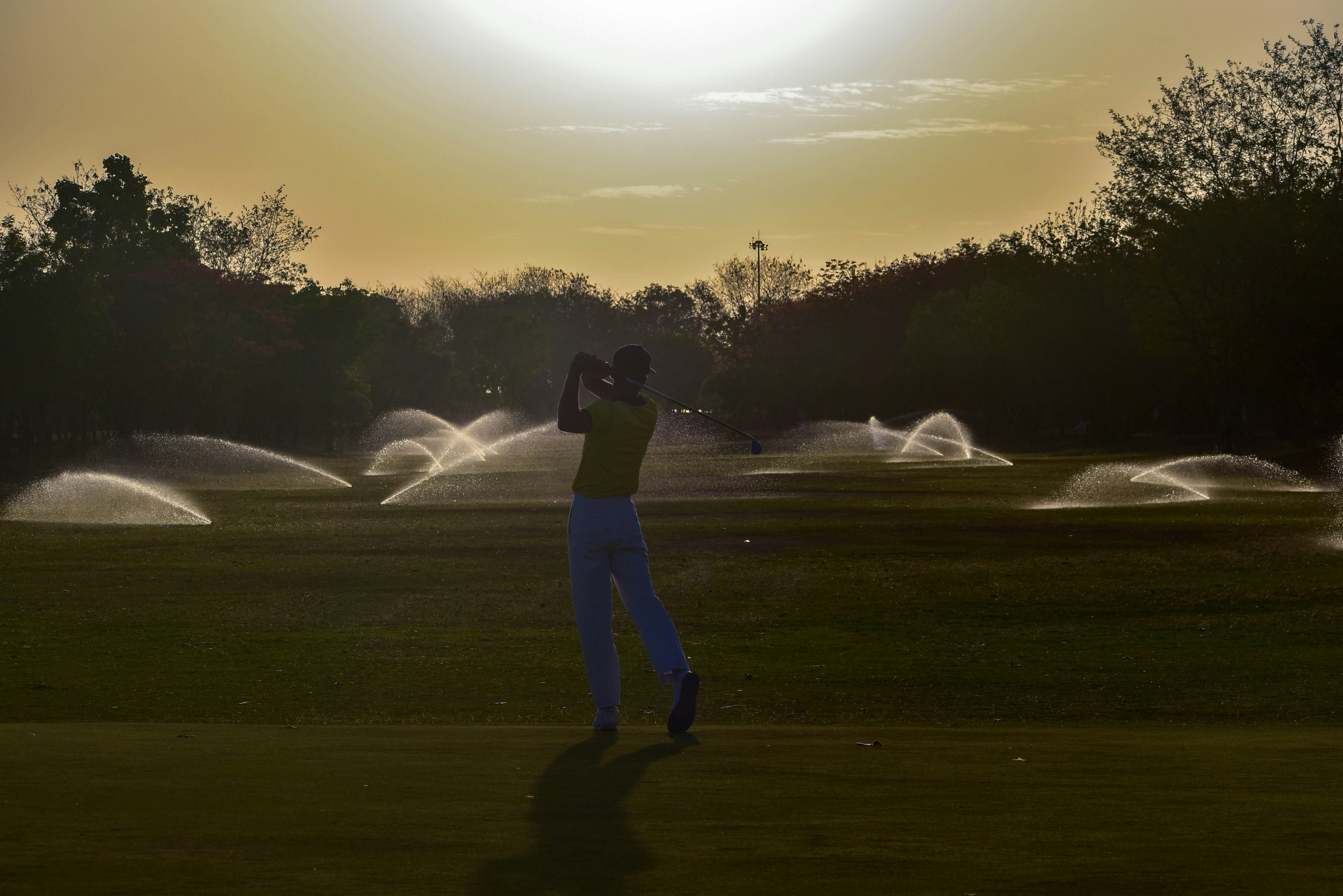 Silhouetted Swing: A Golf Swing Amid Sprinkler Arcs at Dusk