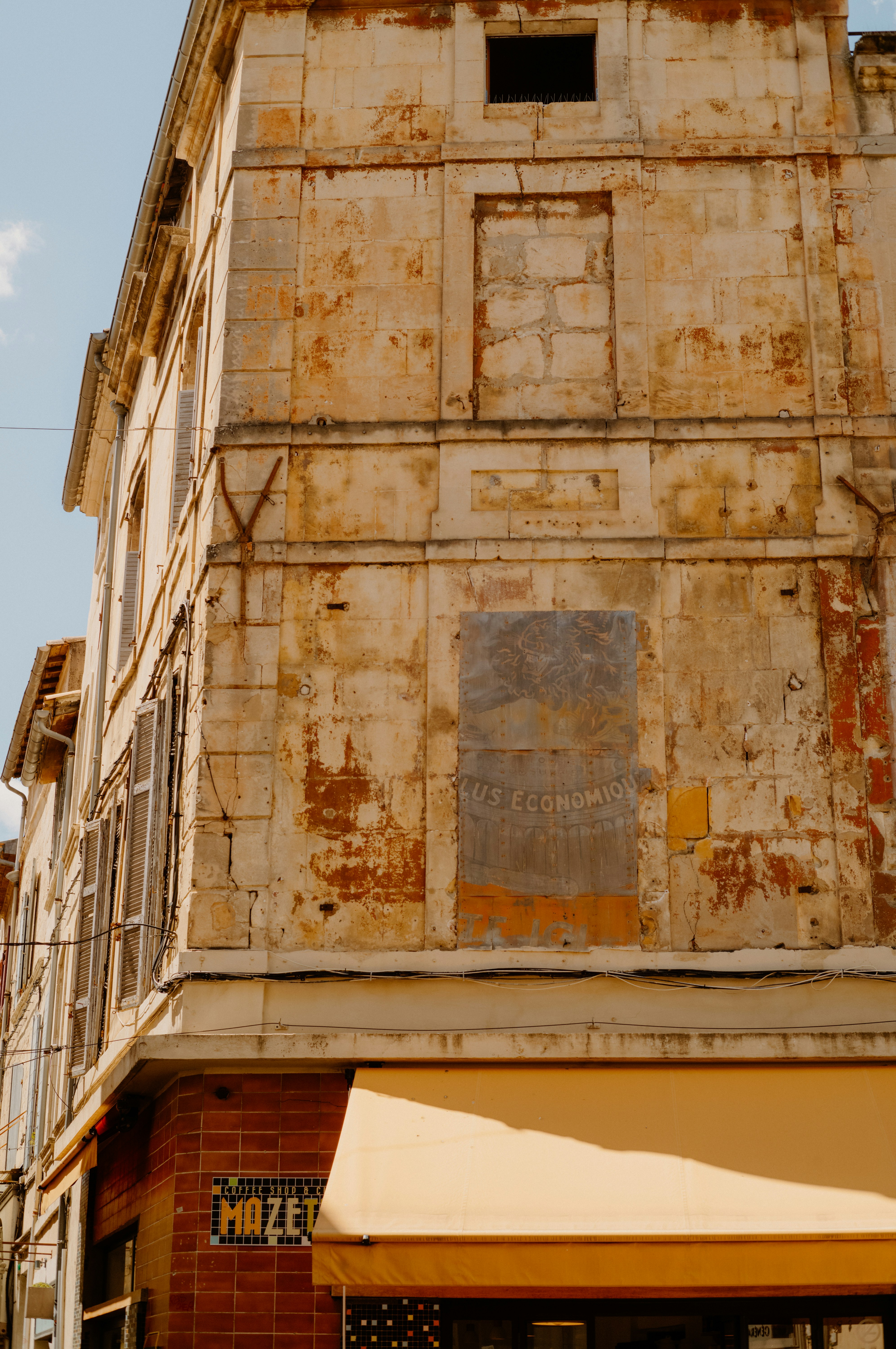 Sunlit storefront on a weathered building corner with peeling plaster and a hanging awning, capturing urban decay and warm tones.