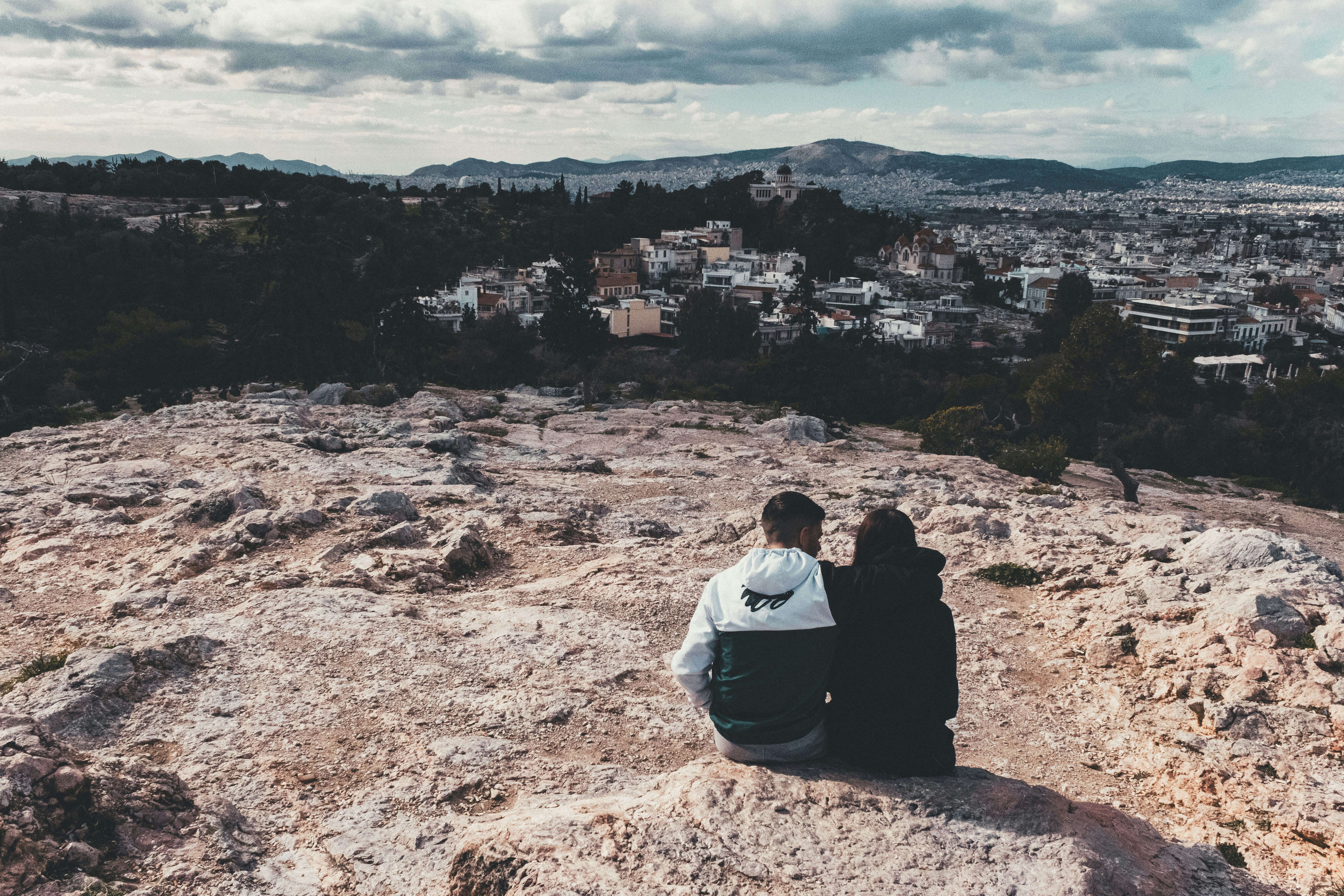 Two Silhouettes on a Rocky Promontory Overlooking a Suburban Crest
