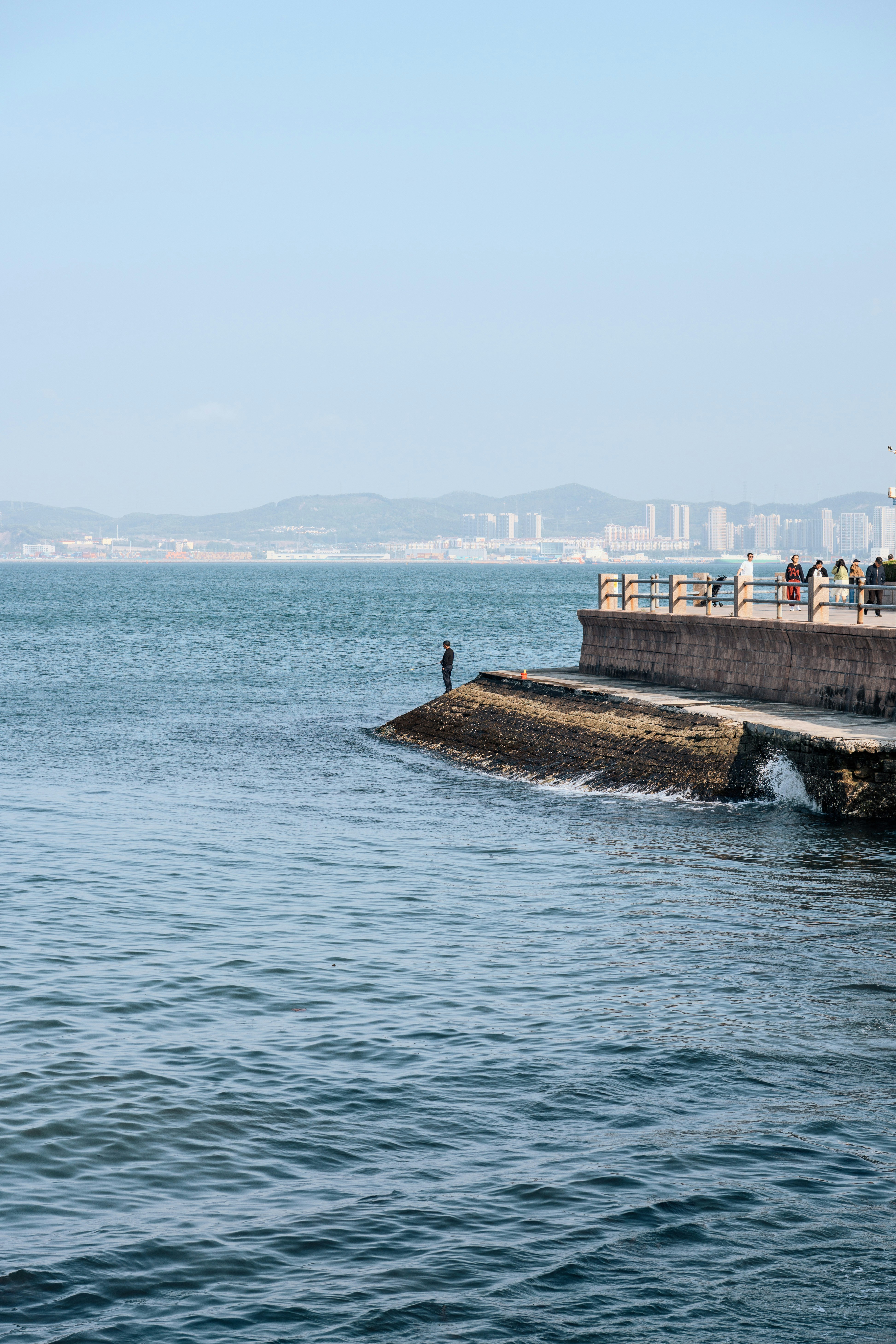 Harbor Edge: A Lone Angler at the Pier as Sea Meets Sky