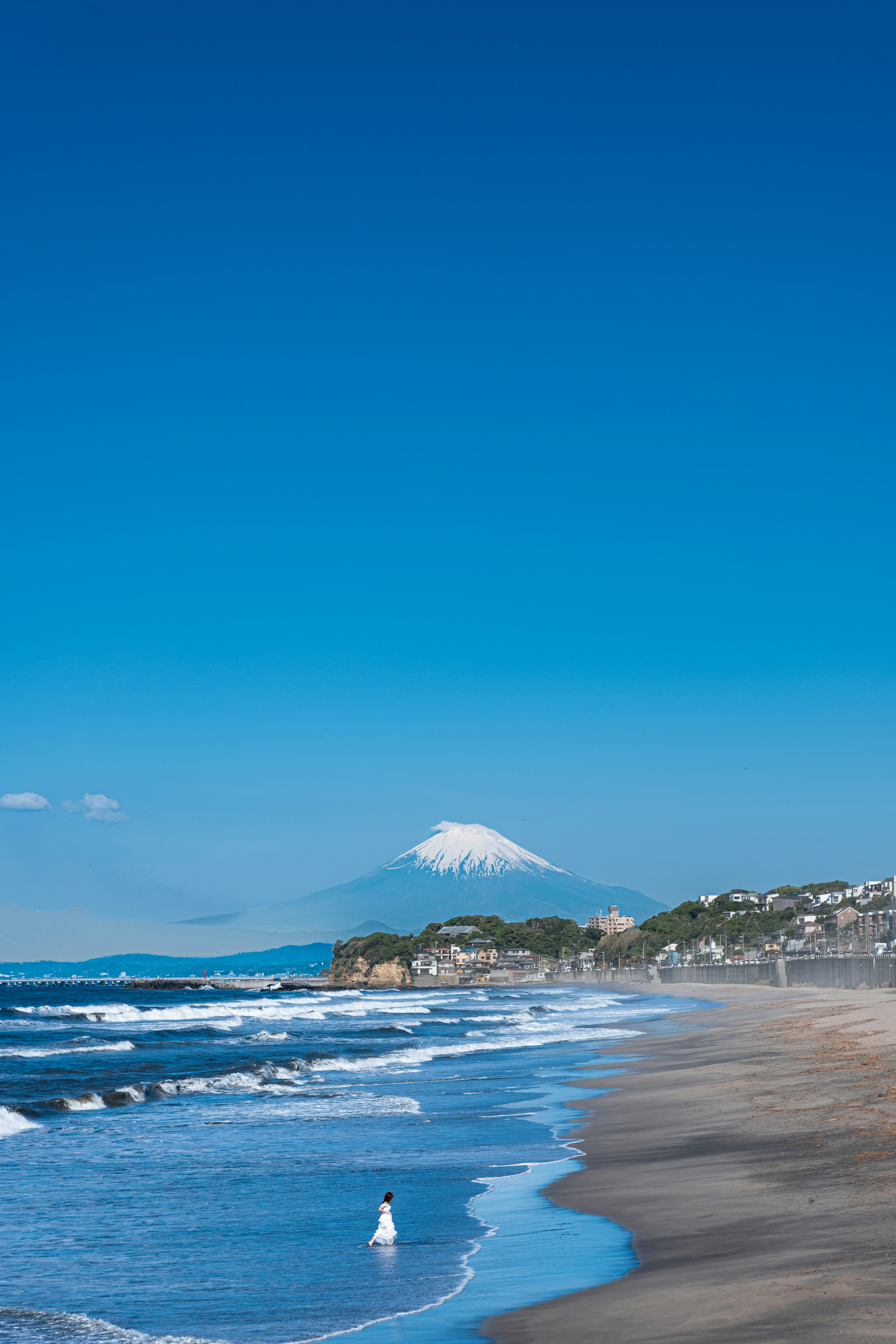 Person walks on a sunny beach with mount fuji.